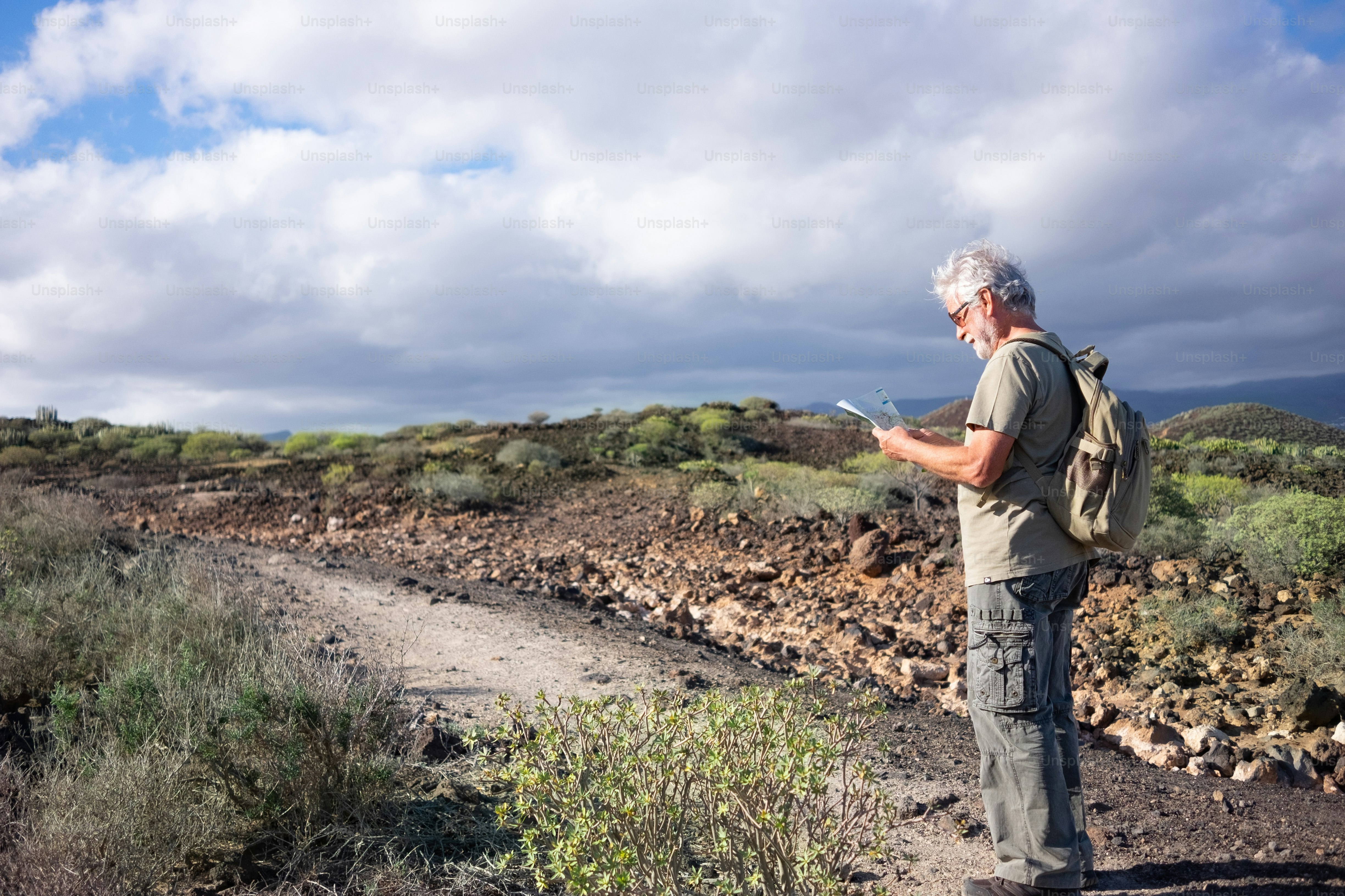 Smiling relaxed senior bearded man in outdoor excursion consulting his ...