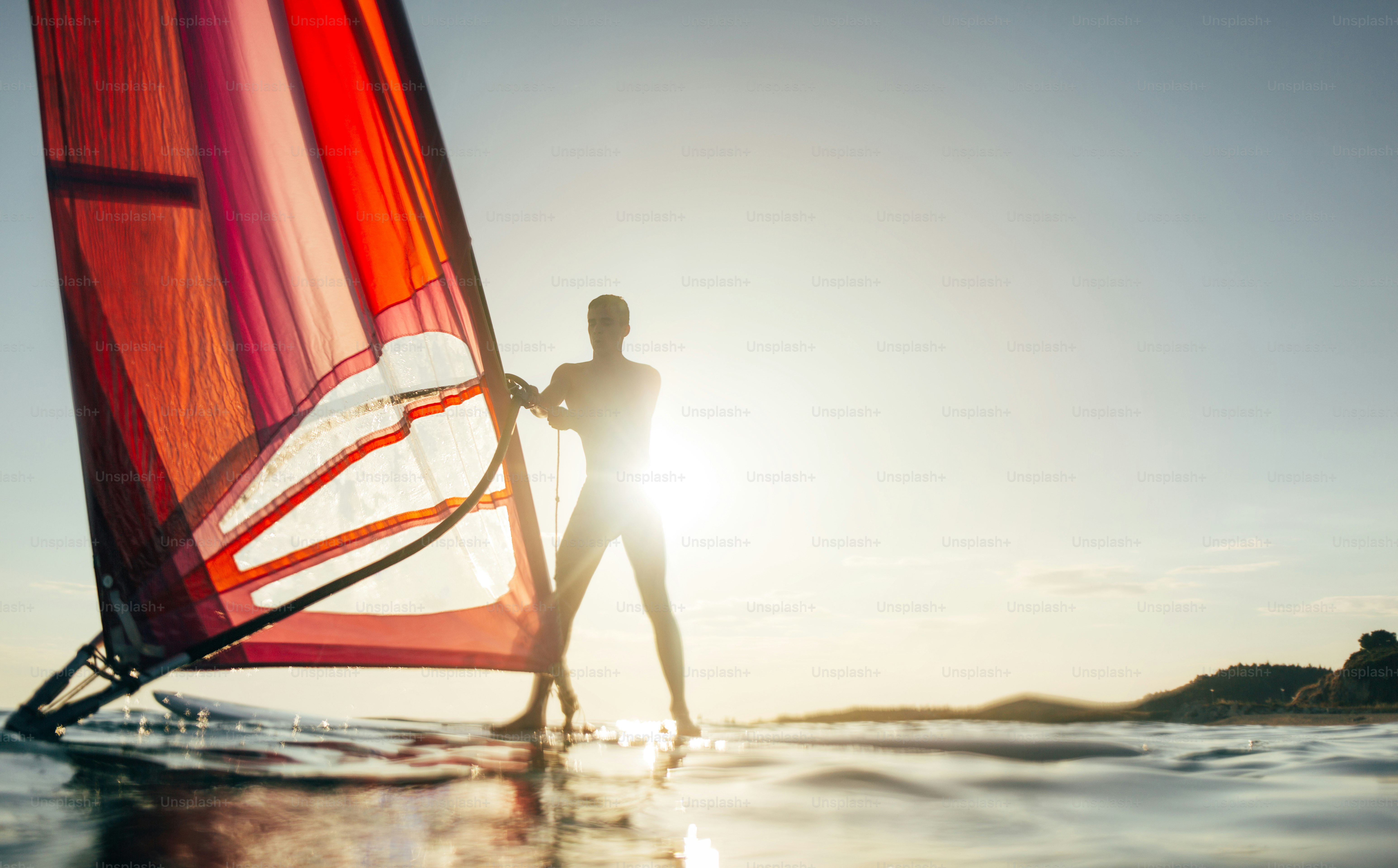 Low angle view of surfer silhouette balancing on windsurf board ...