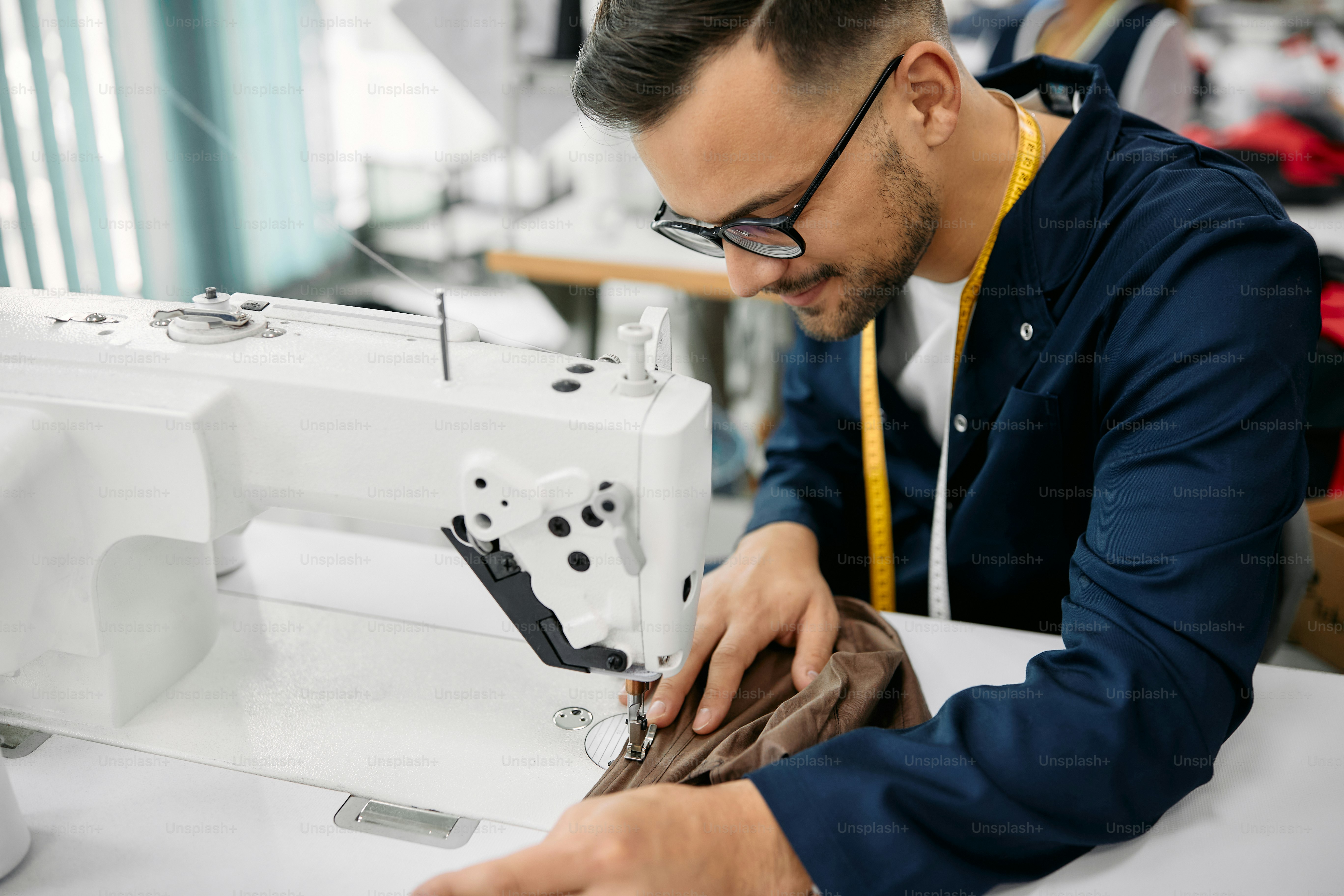 Smiling textile worker working with sewing machine at clothing design ...