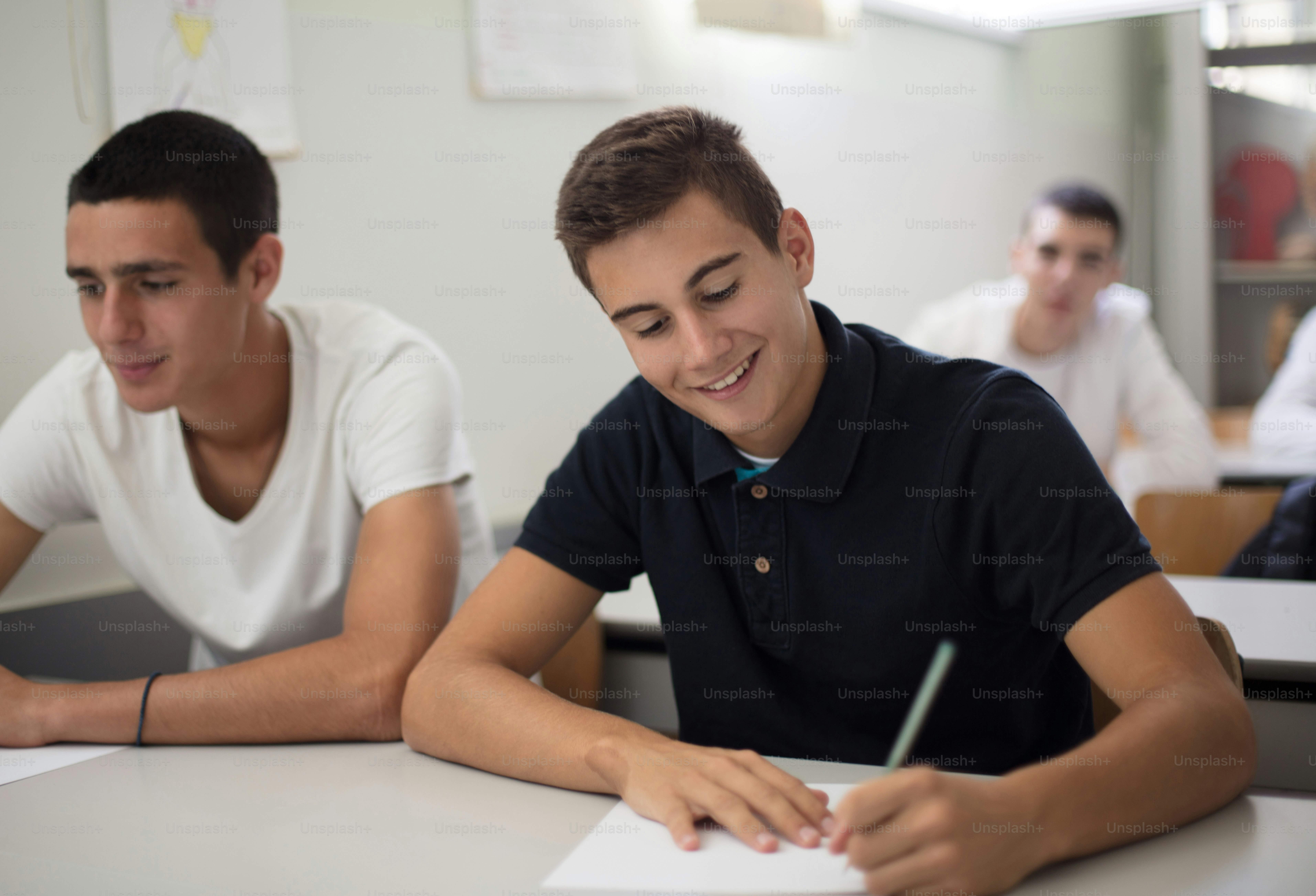 Exam. Teenagers students sitting in the classroom and writing. Focus is ...