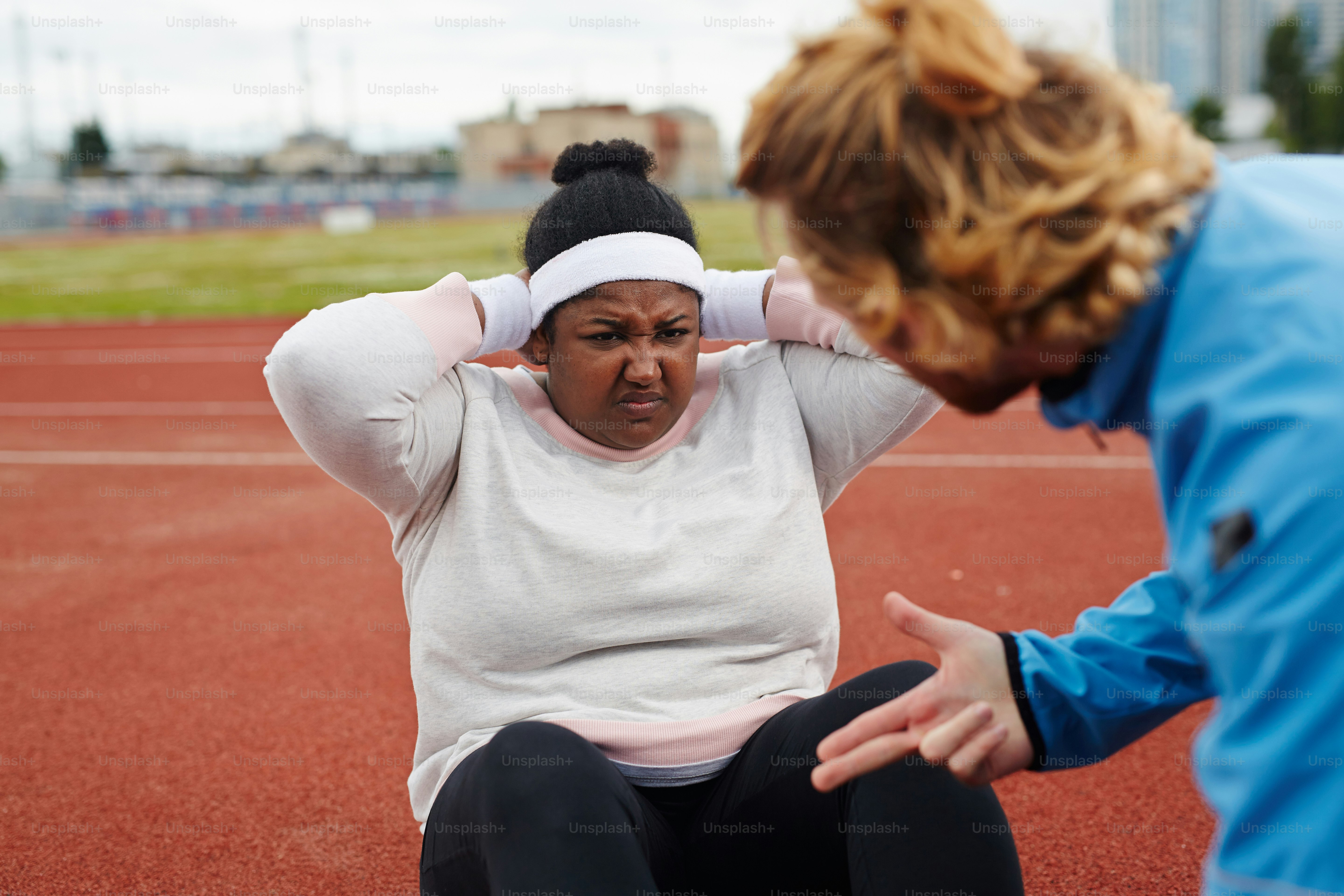 Determined plus-sized woman doing difficult exercise with her trainer ...