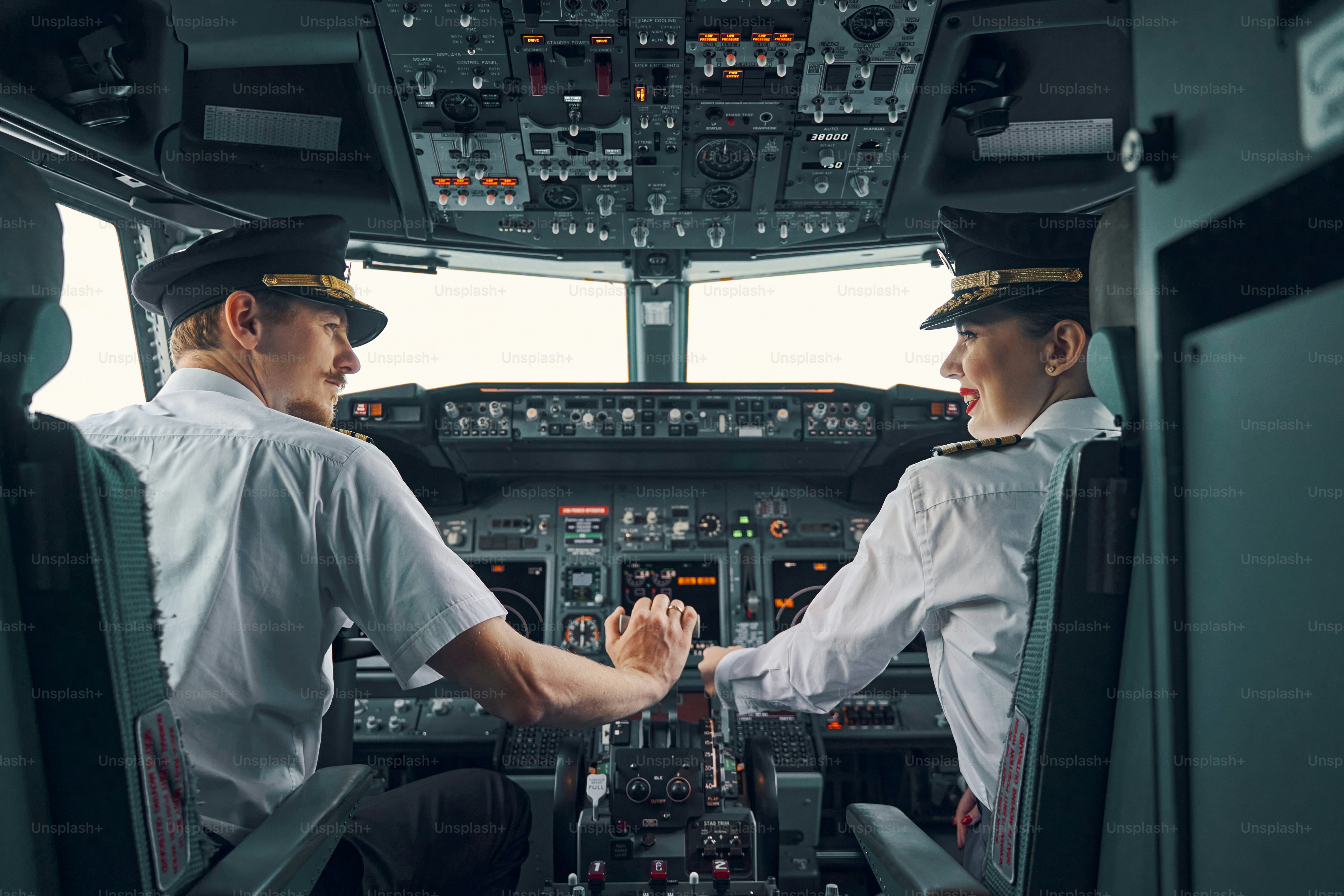 Back view of a pleased female co-pilot smiling at a serious airline ...