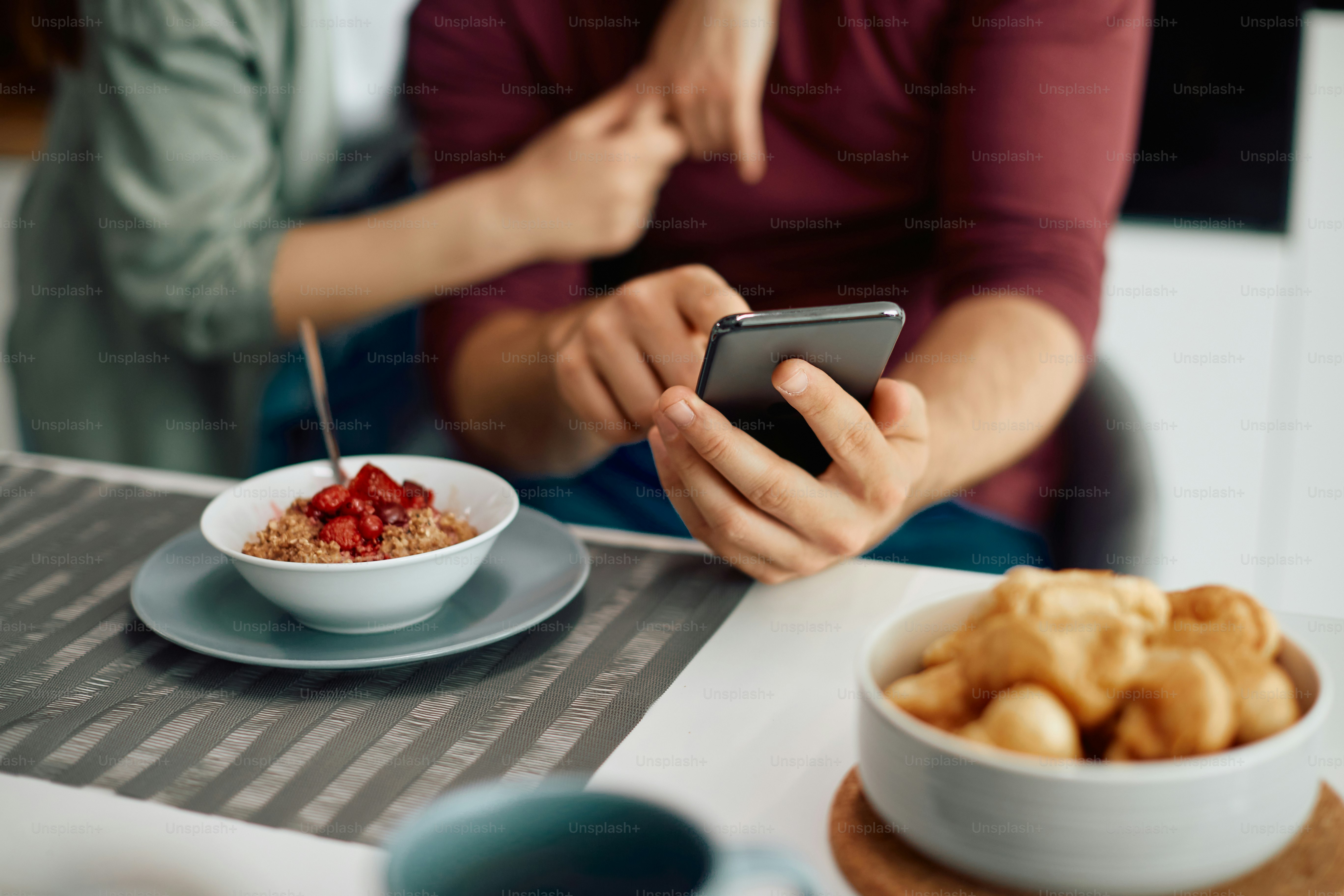 Close-up of couple using using smart phone while having breakfast at ...