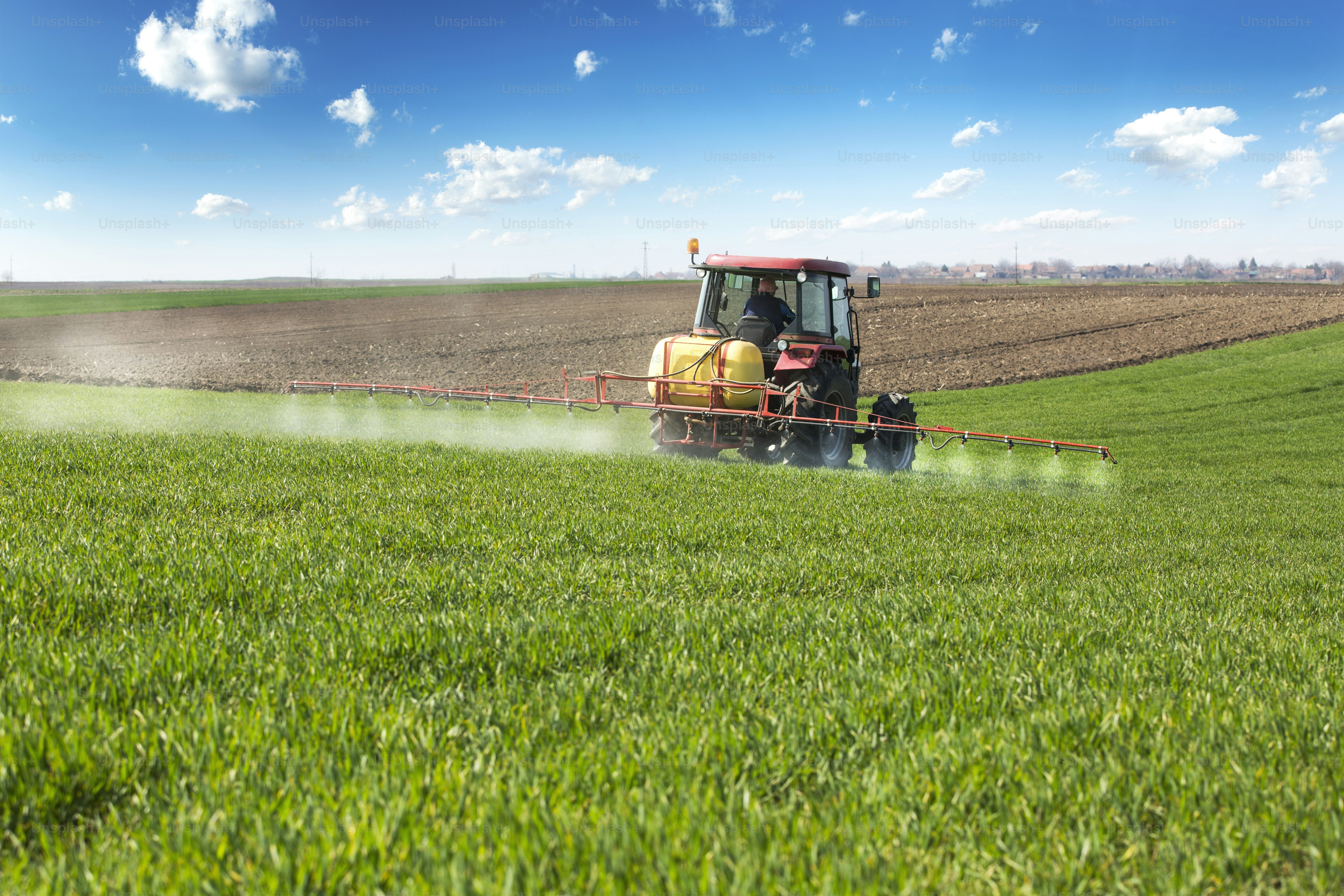 Farmer spraying wheat field with tractor sprayer at spring season photo ...