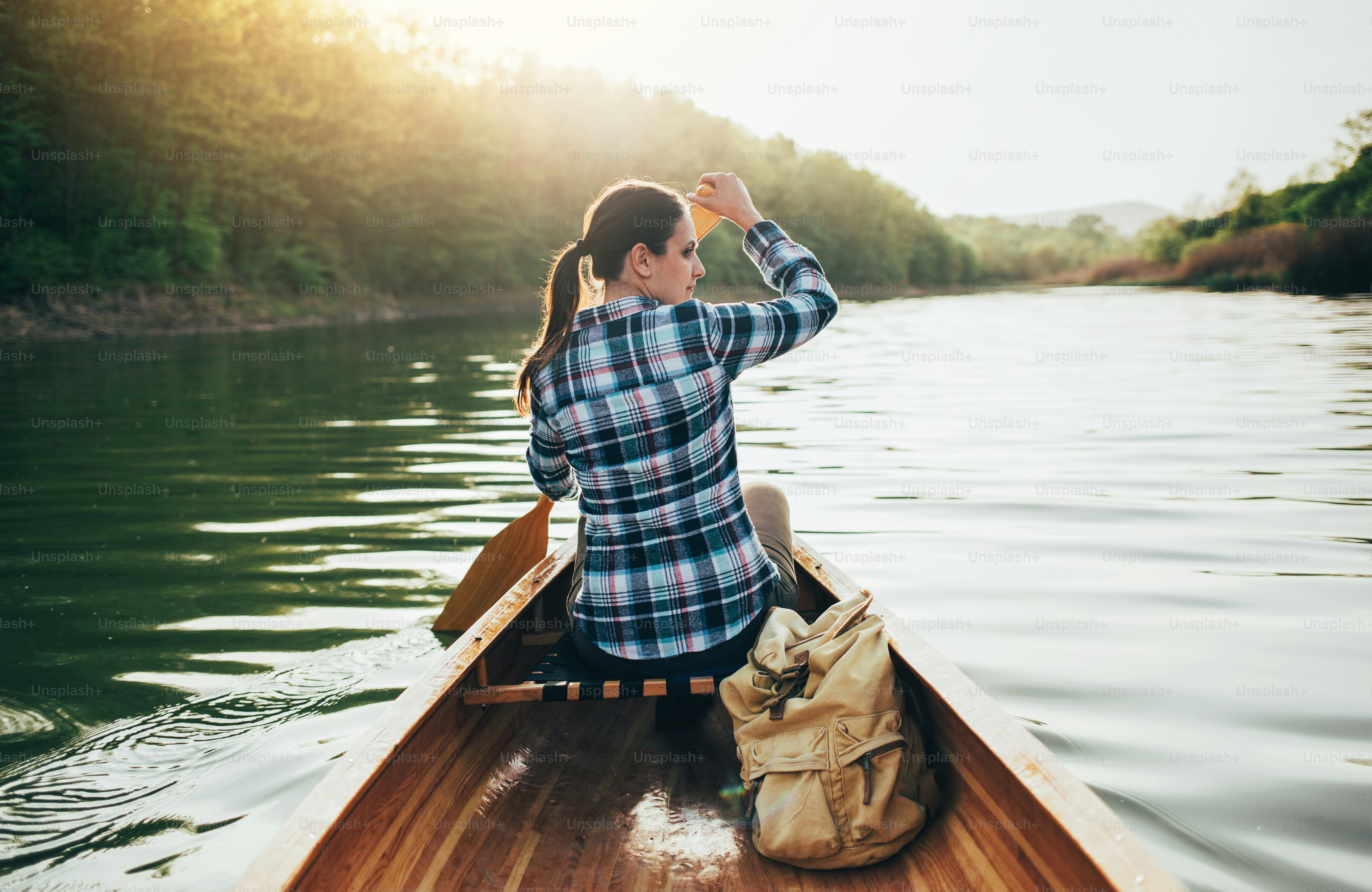 Rear view of hipster girl paddling the canoe on the sunset lake. photo ...