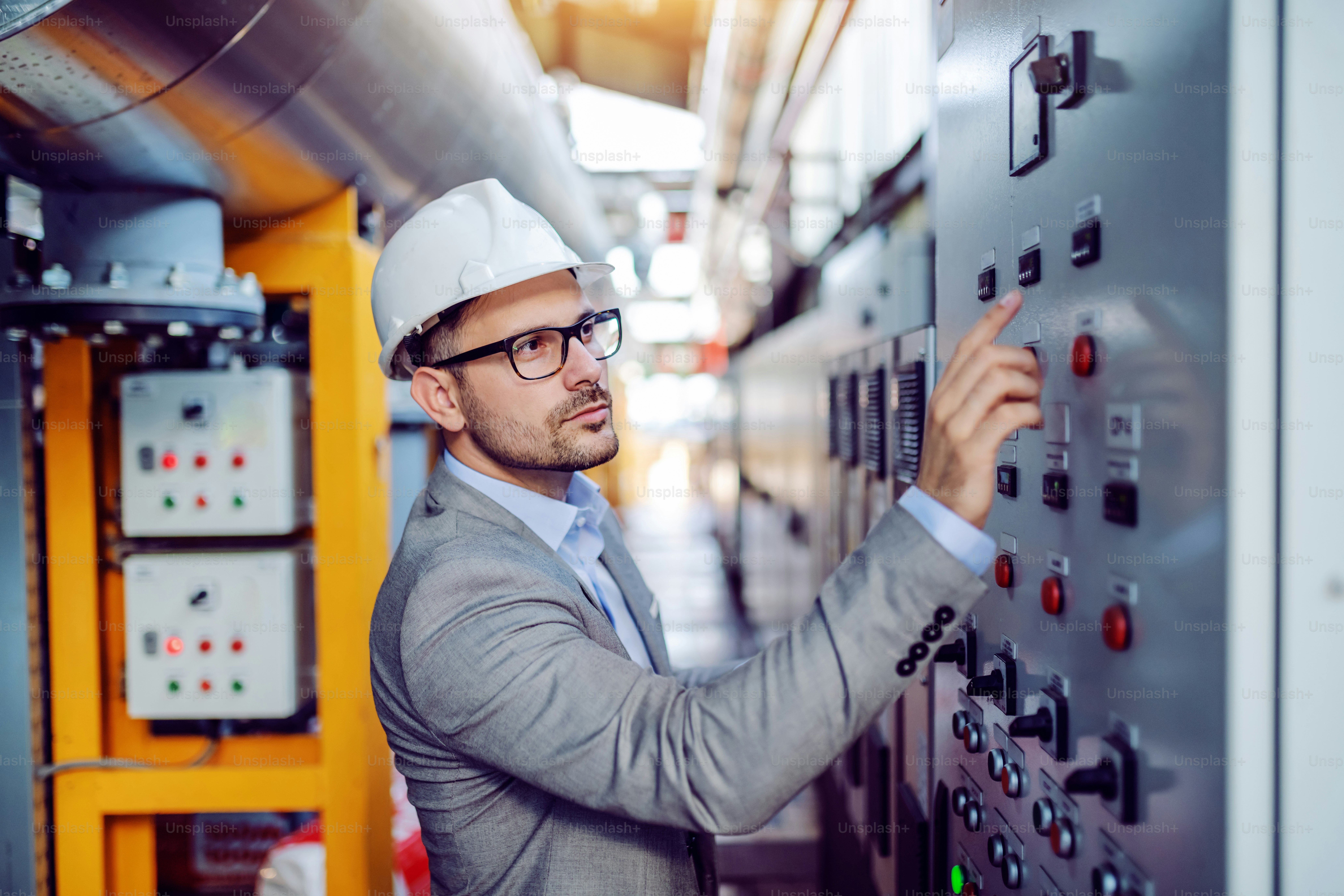 Serious handsome caucasian supervisor in gray suit and with helmet on ...