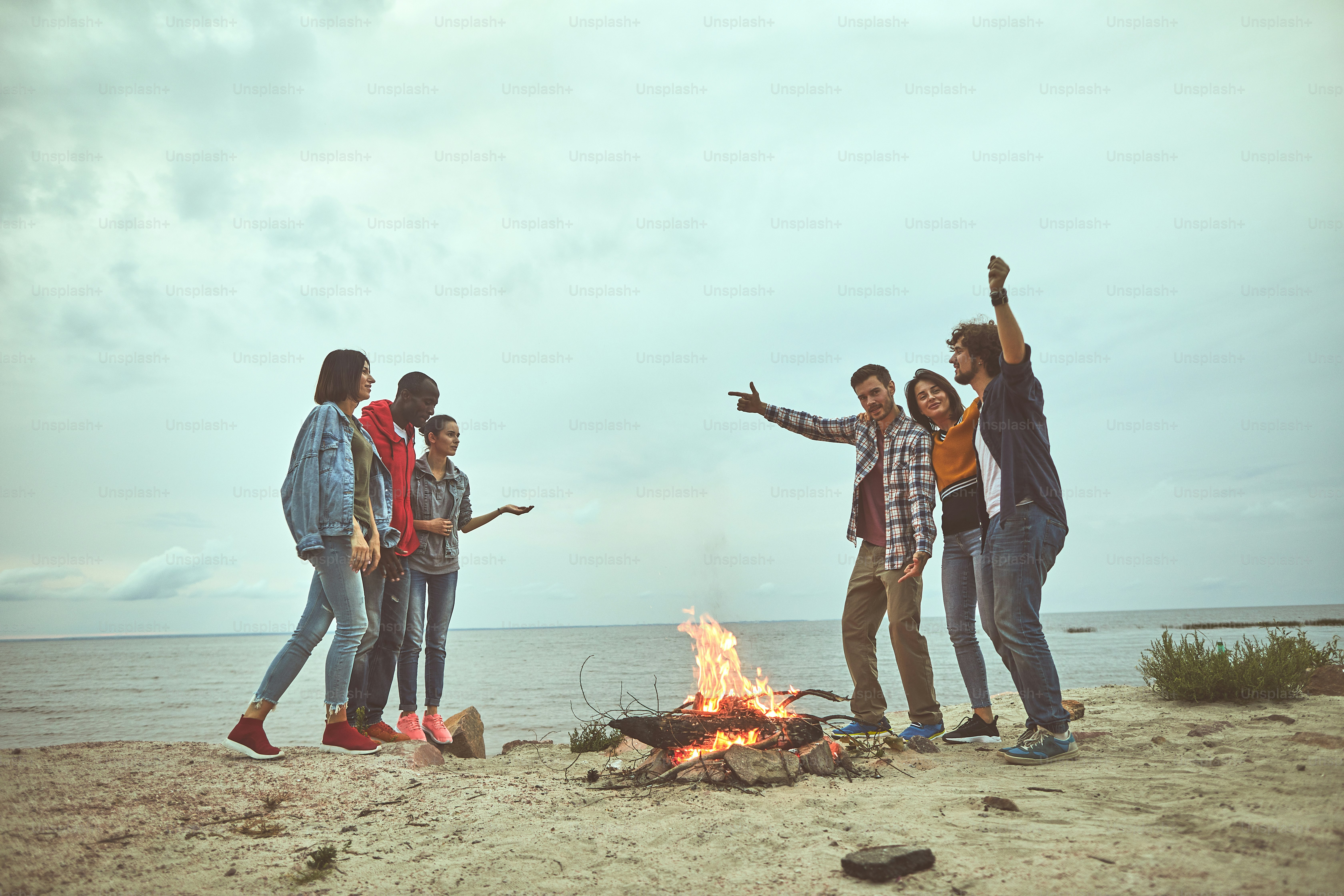 Get together. Happy friends standing near bonfire while telling stories ...