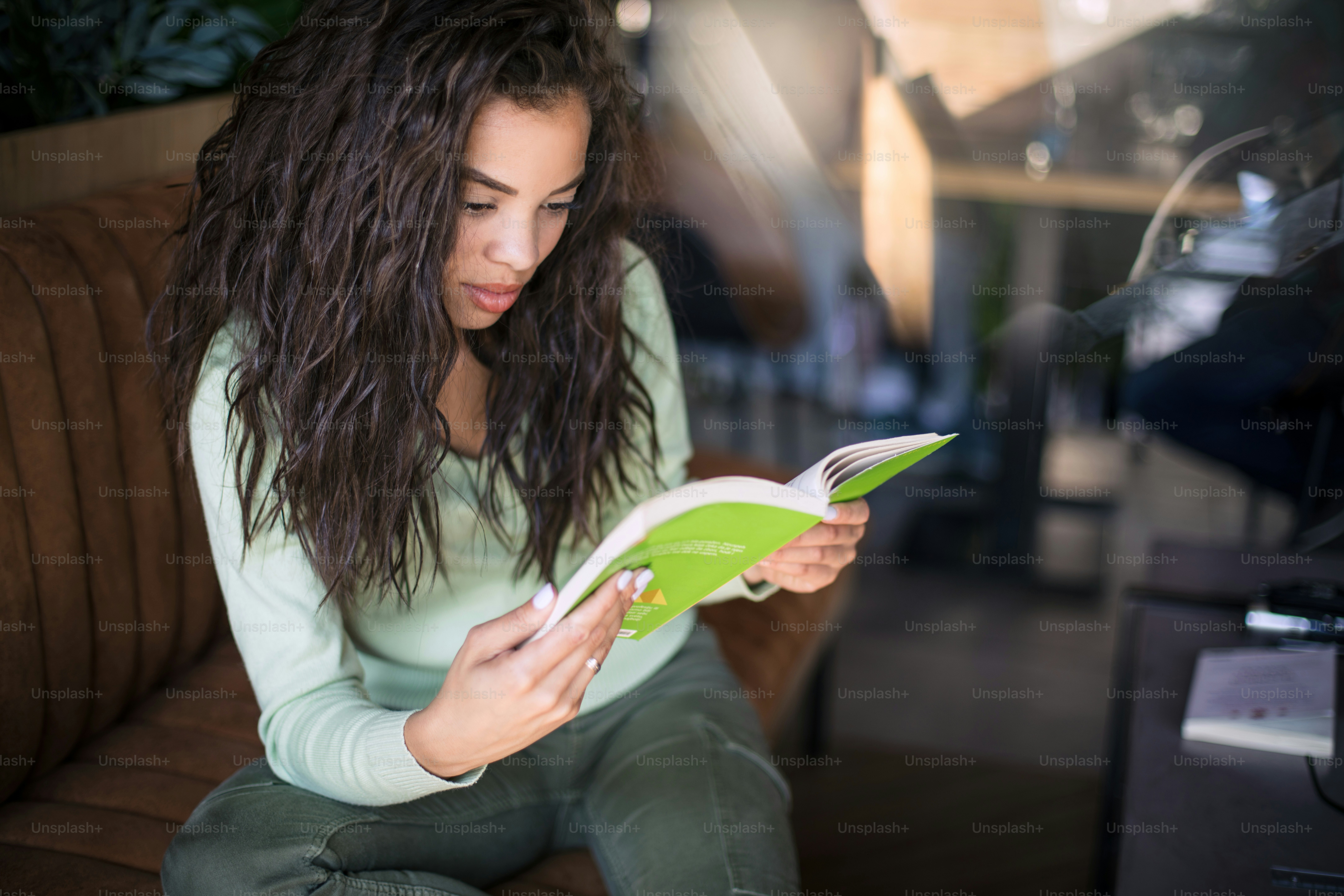 Through reading we learn new things. Young student girl at cafe reading ...