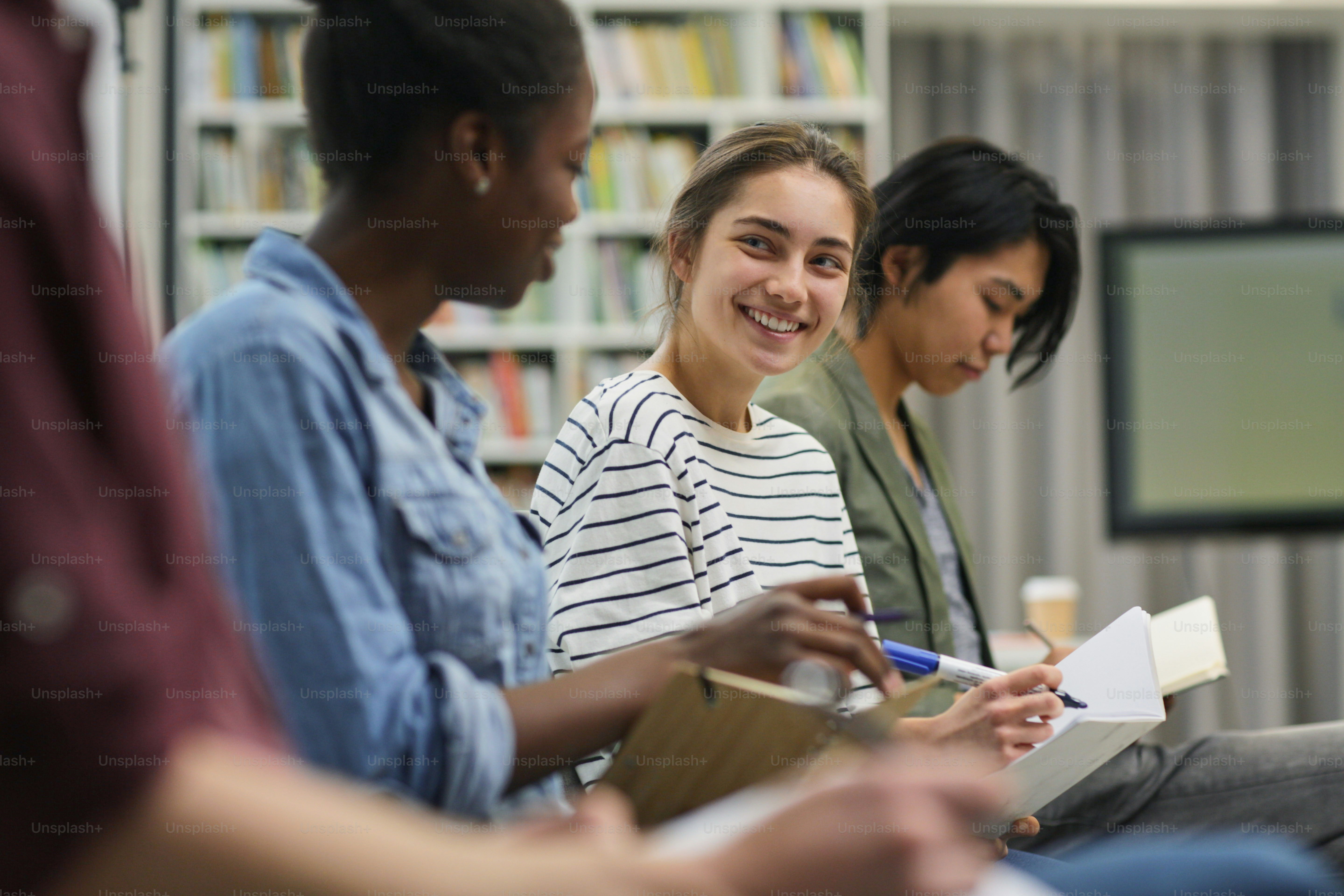 Group of students sitting and talking to each other while writing ...