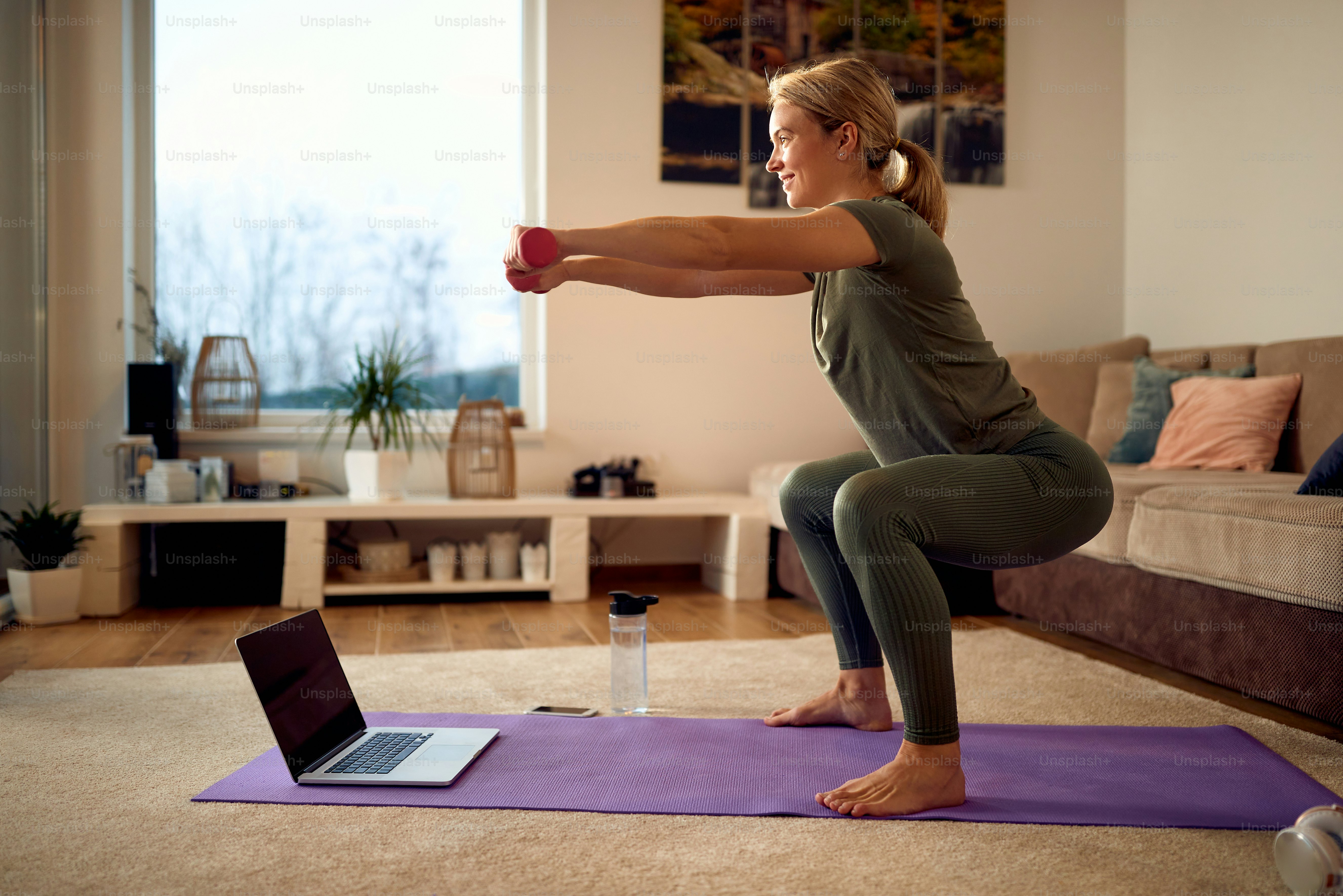 Happy sportswoman practicing squats while using hands weights during ...