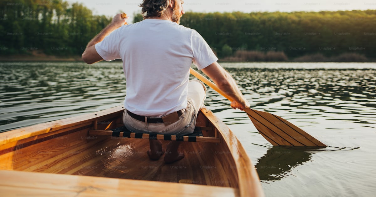 Rear view of male canoeist paddling the wooden canoe with oar. photo ... Rear view of male canoeist paddling the wooden canoe with oar. photo ...