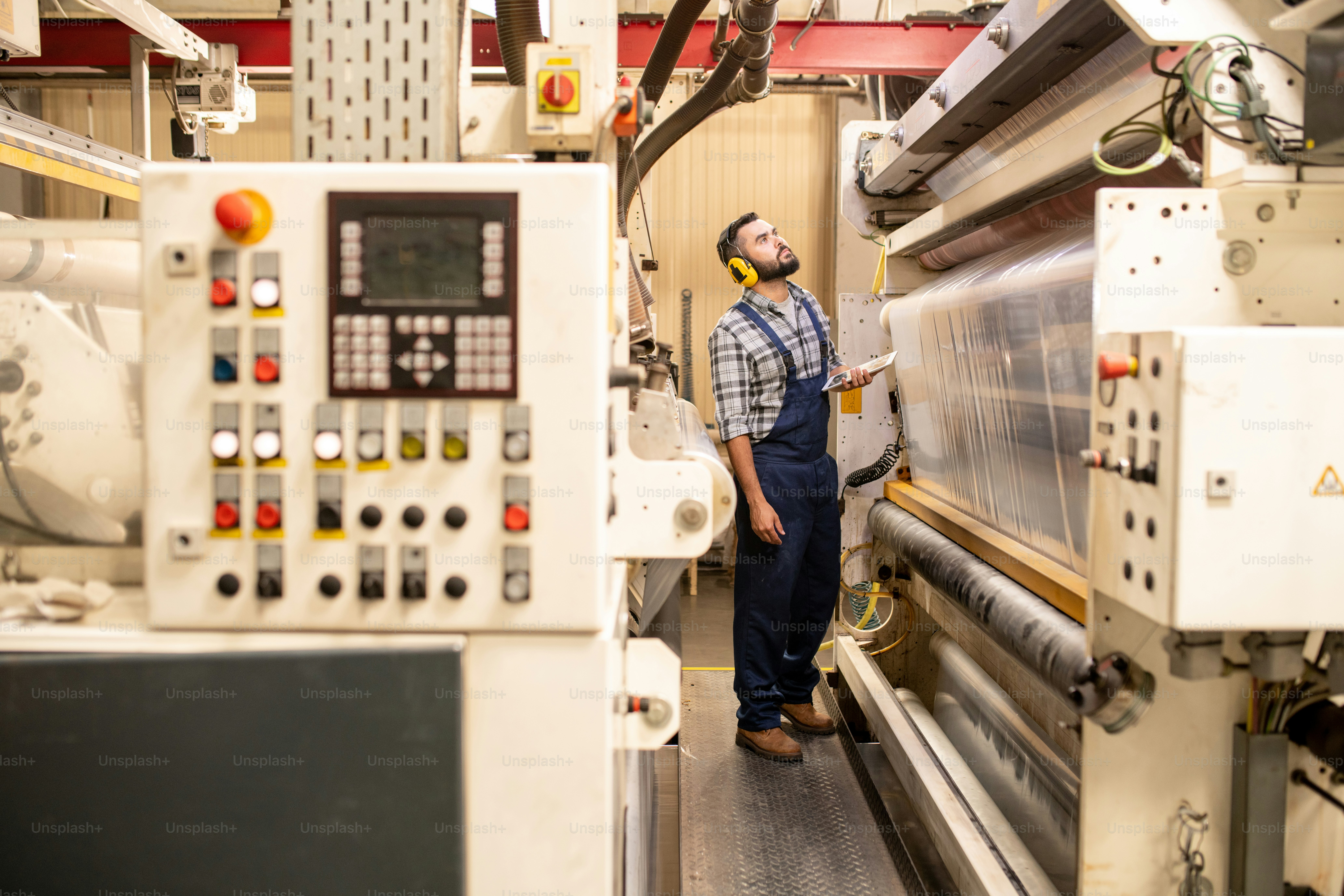 Young production control engineer in workwear and protective headphones ...