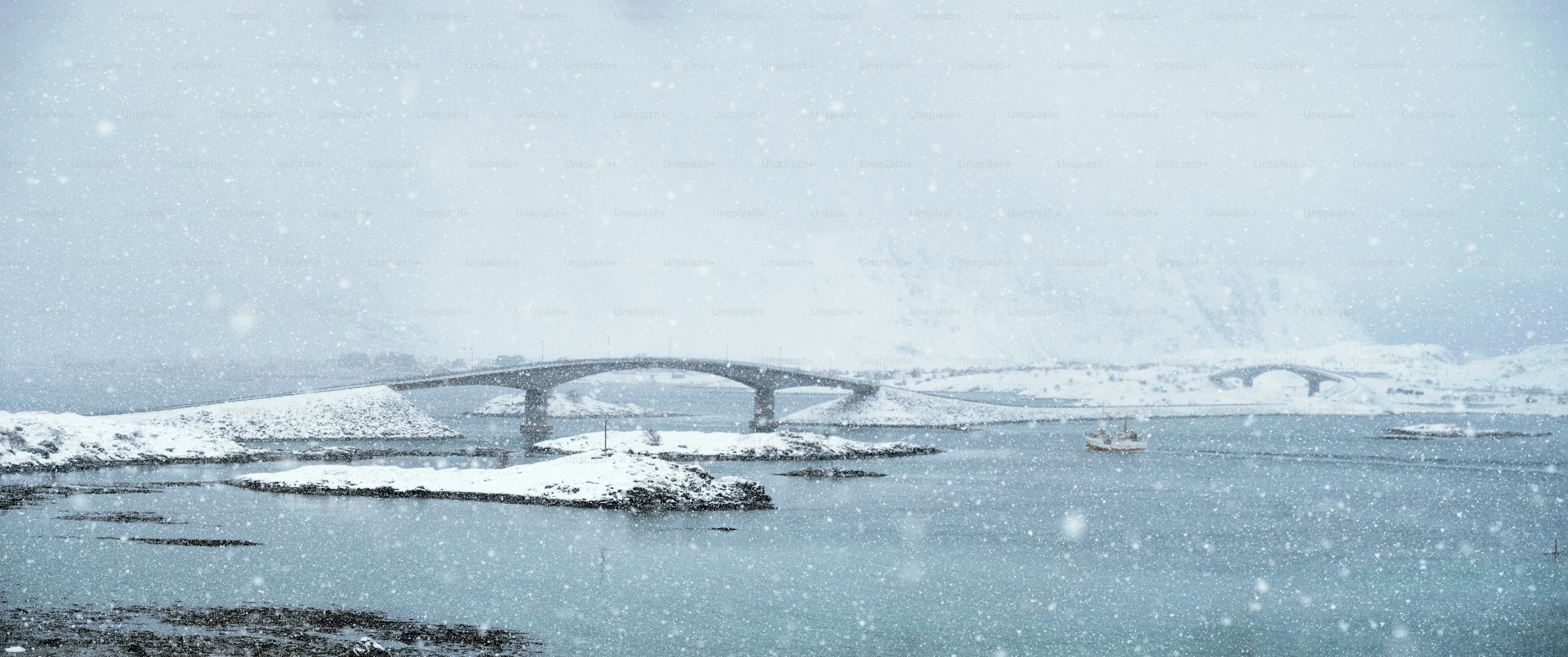 Fredvang bridges in heavy snowfall in winter with fishing ship. Lofoten ...