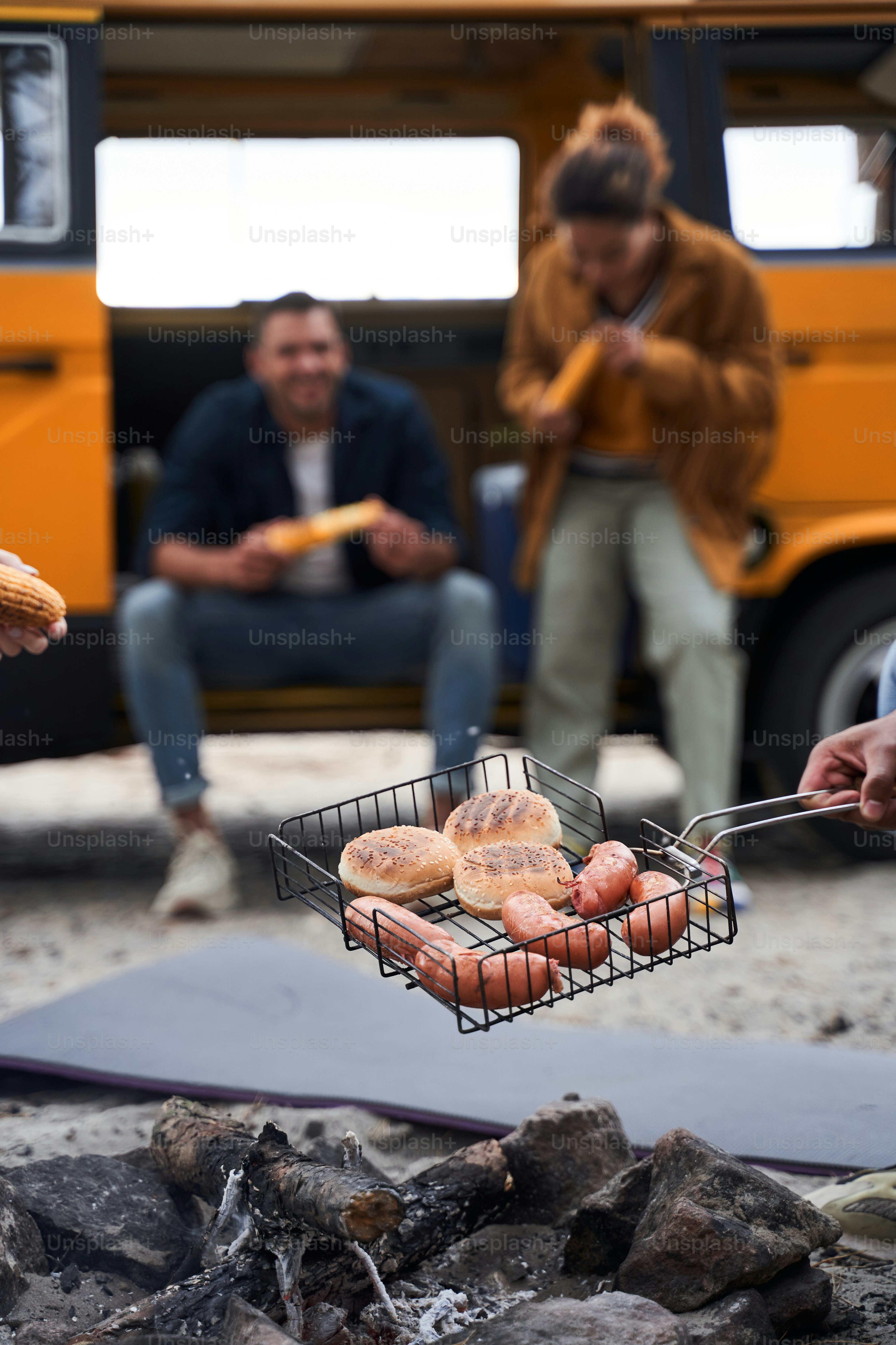 Group of tourists preparing their lunch in the forest. Focus on sausage ...
