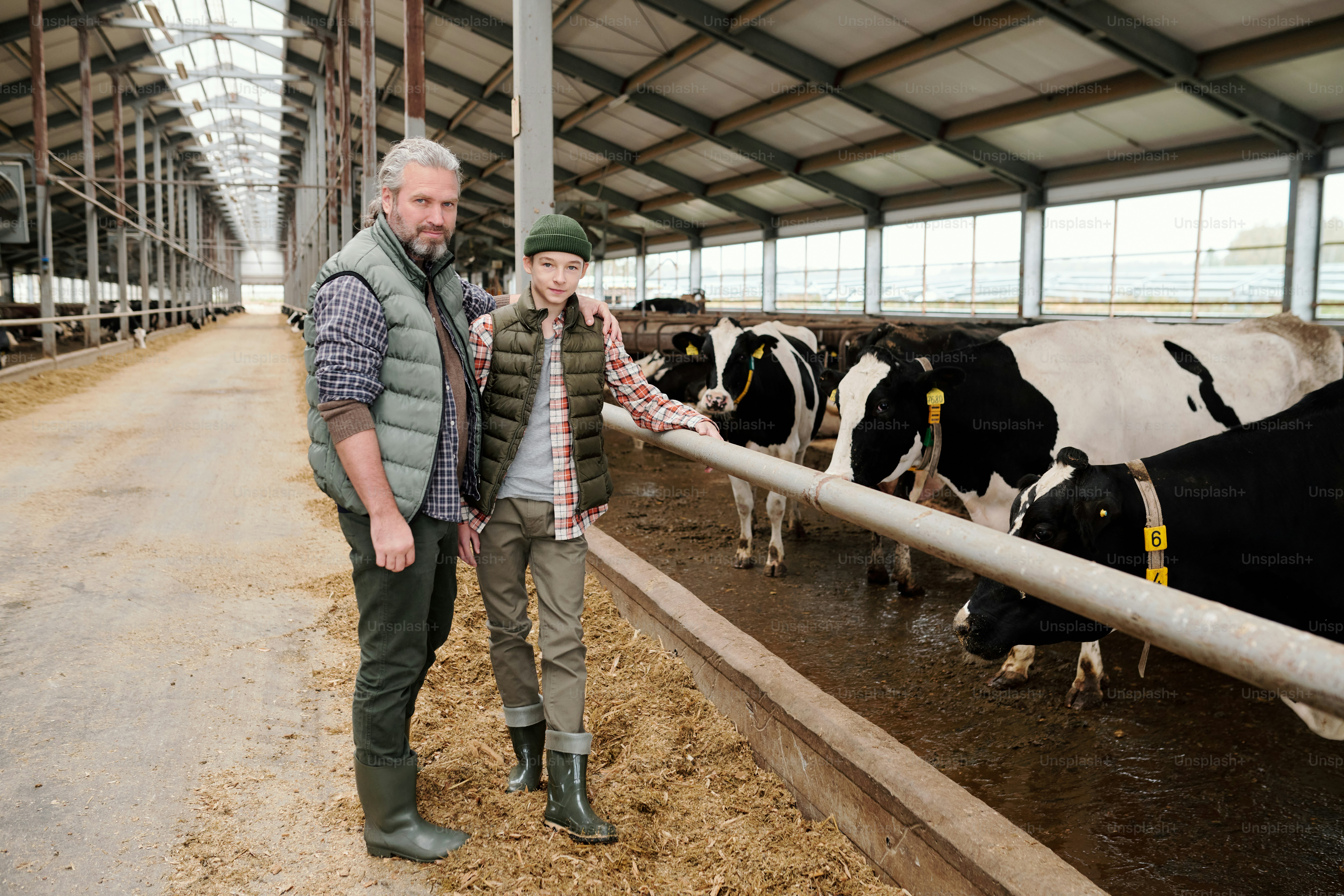 Mature man and teenage boy in workwear looking at you while standing by ...