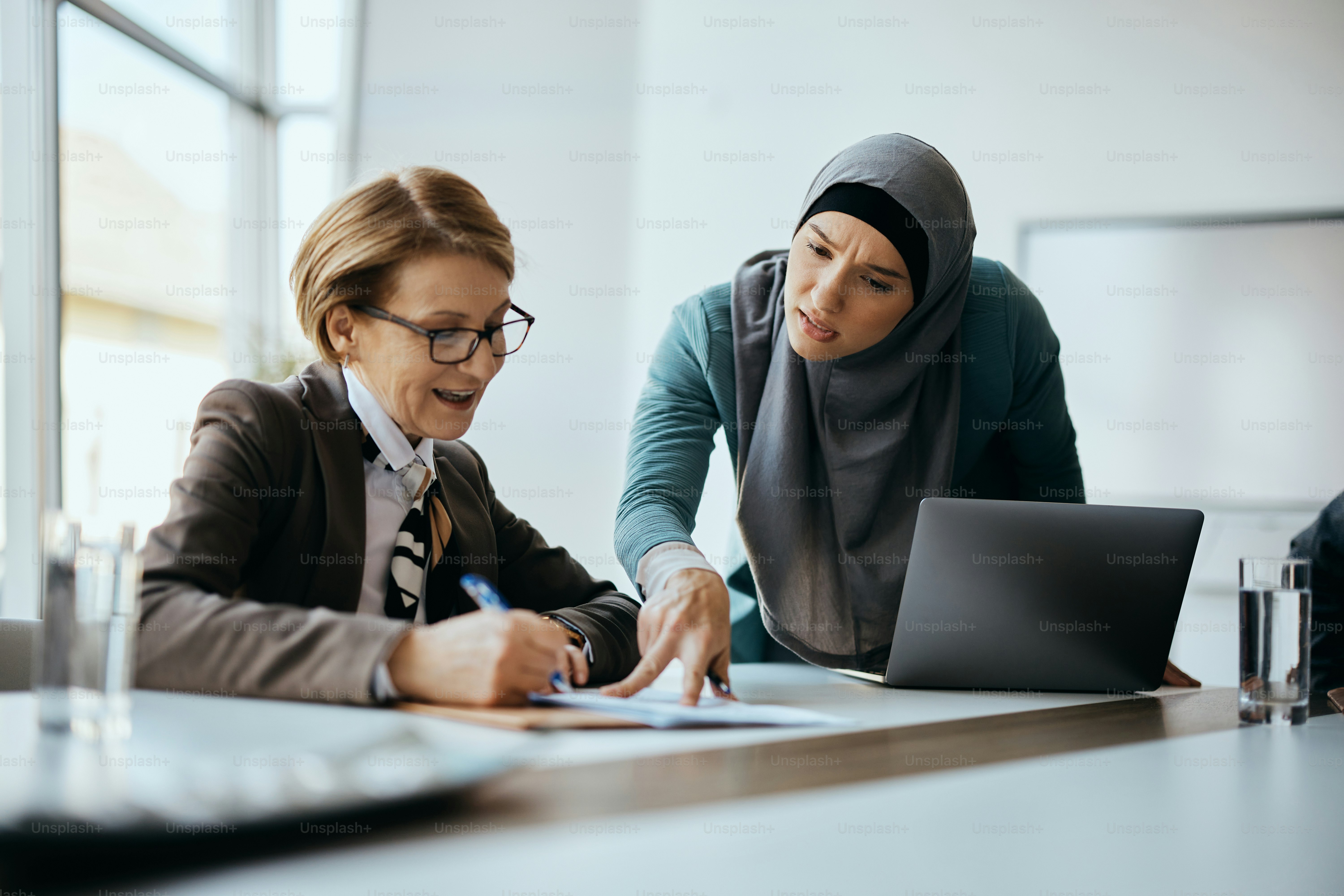 Young Muslim businesswoman and her Caucasian coworker cooperating while ...