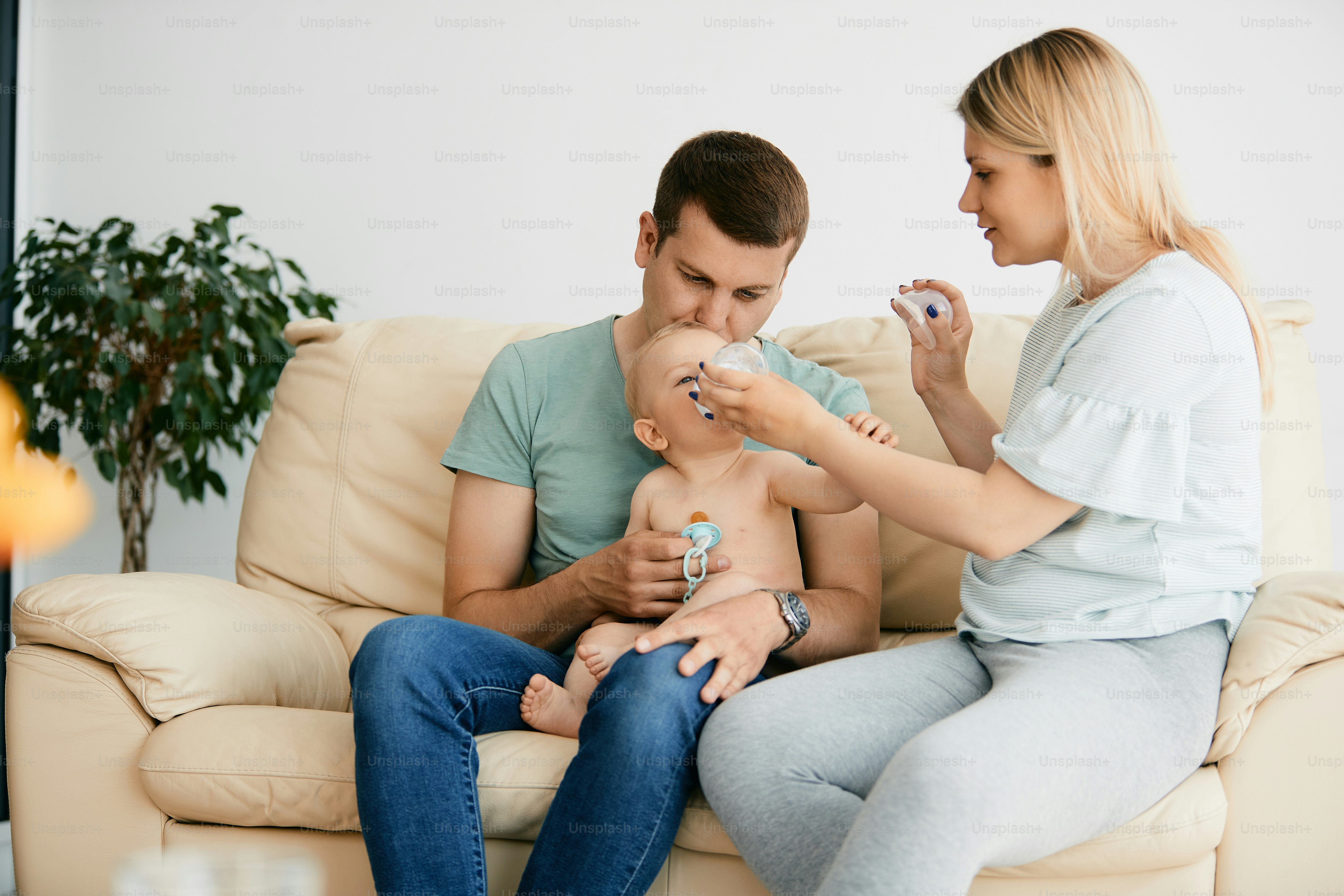Jeune père tenant bébé pendant que sa mère le nourrit avec un biberon à ...