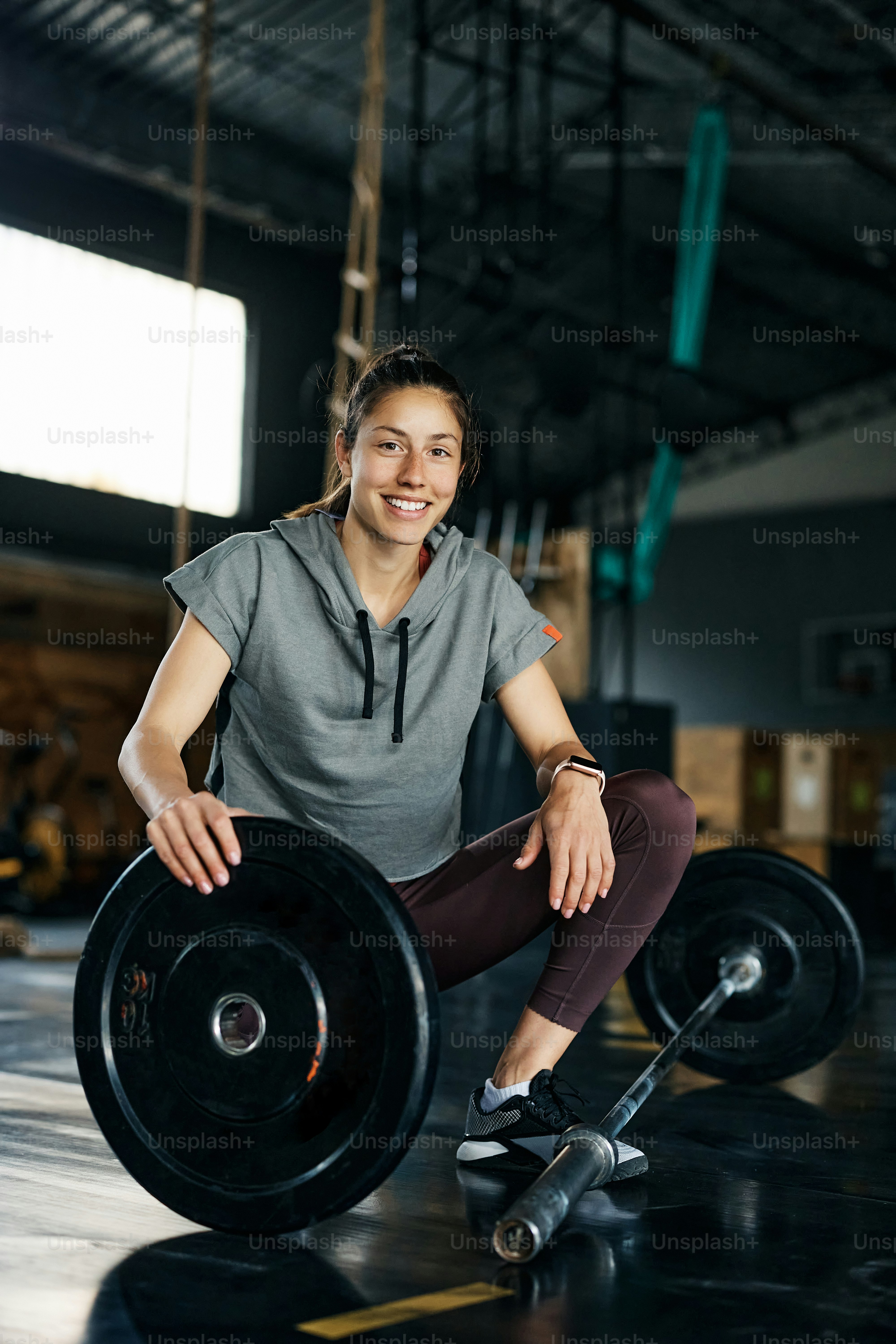 Young happy athletic woman putting weight disk on barbell before ...