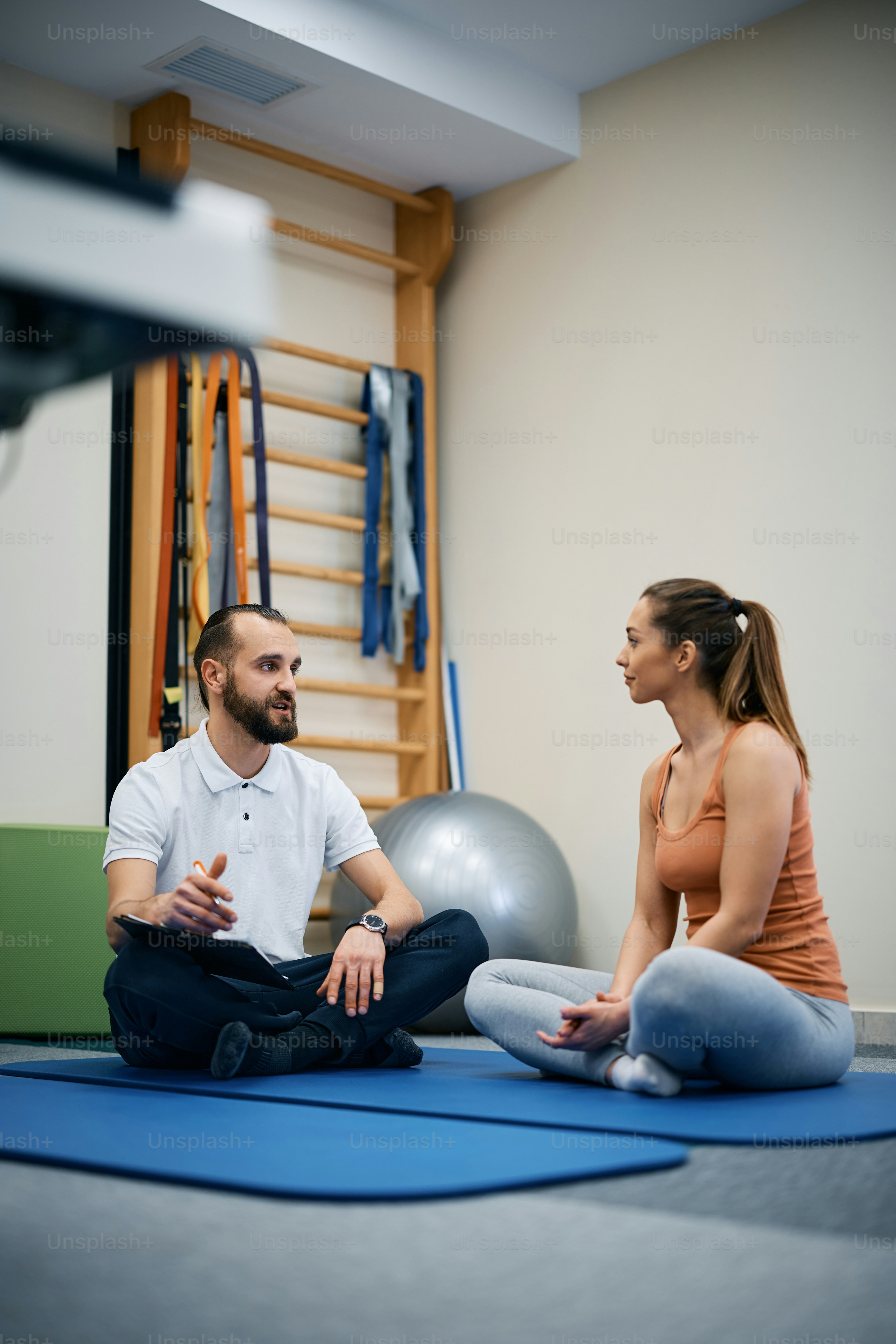 Kinésithérapeute et femme athlétique parlant assise sur le sol dans un ...