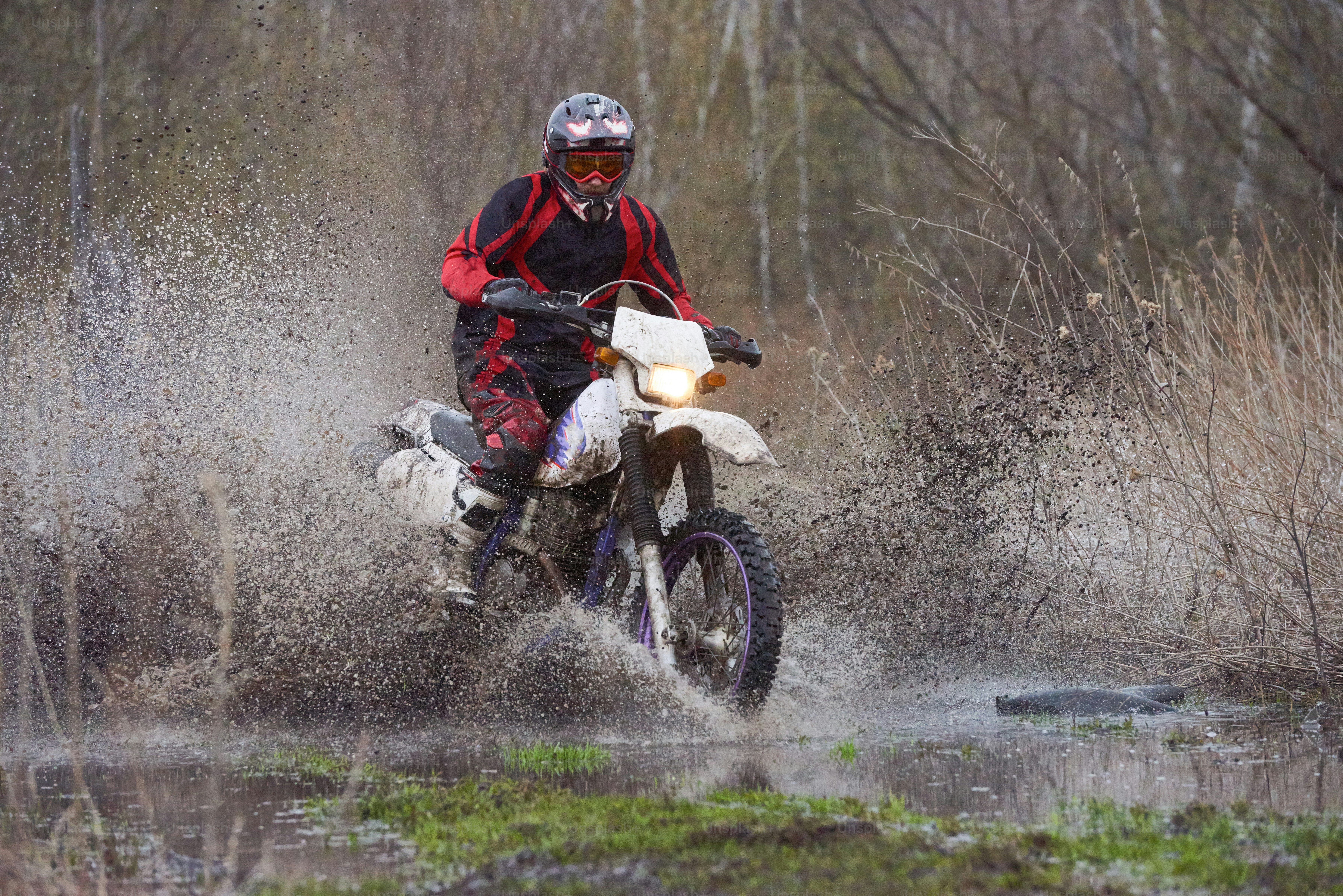 Motorcross rider racing in flooded wood down road with big puddles ...