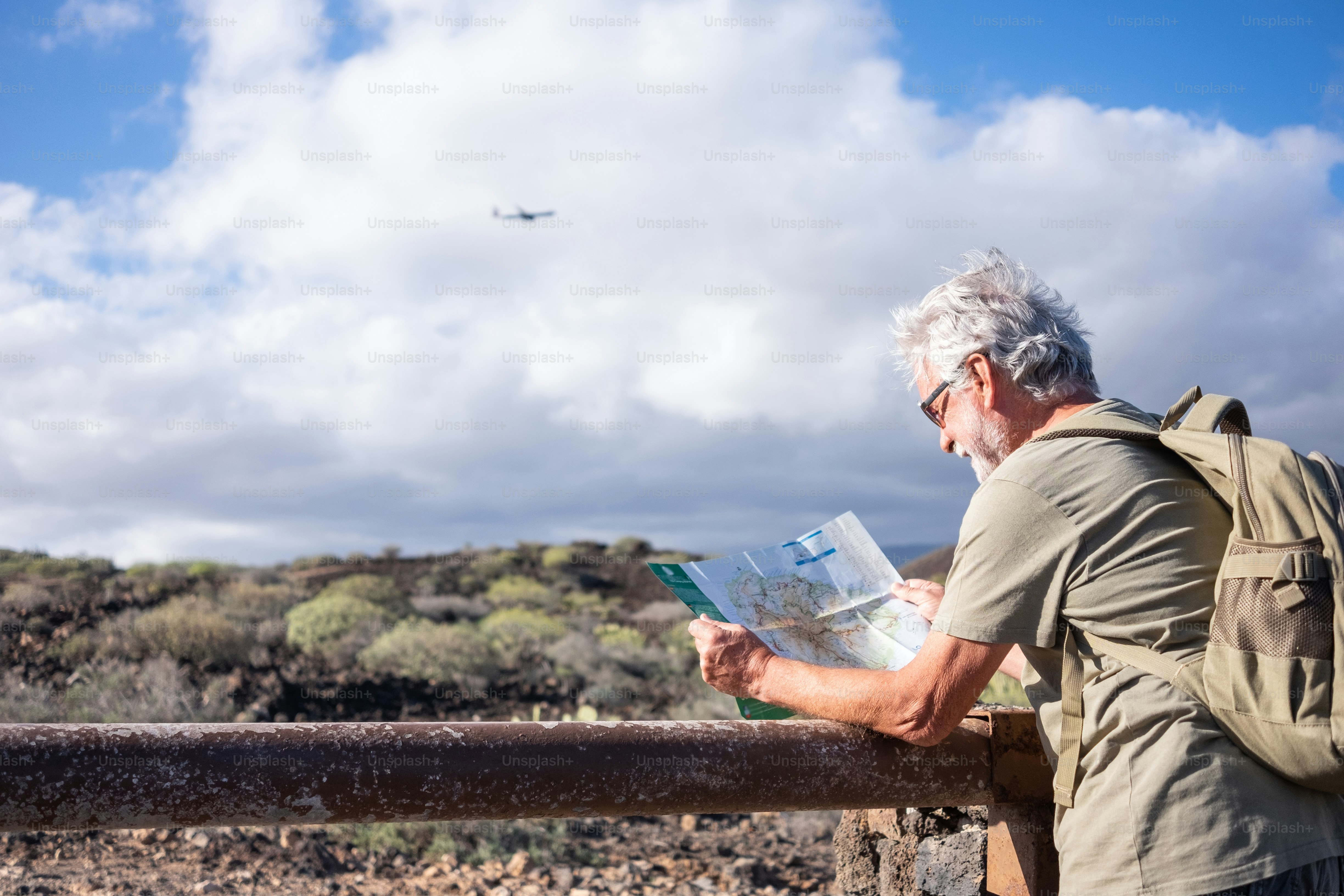 Smiling relaxed senior bearded man in outdoor excursion consulting his ...
