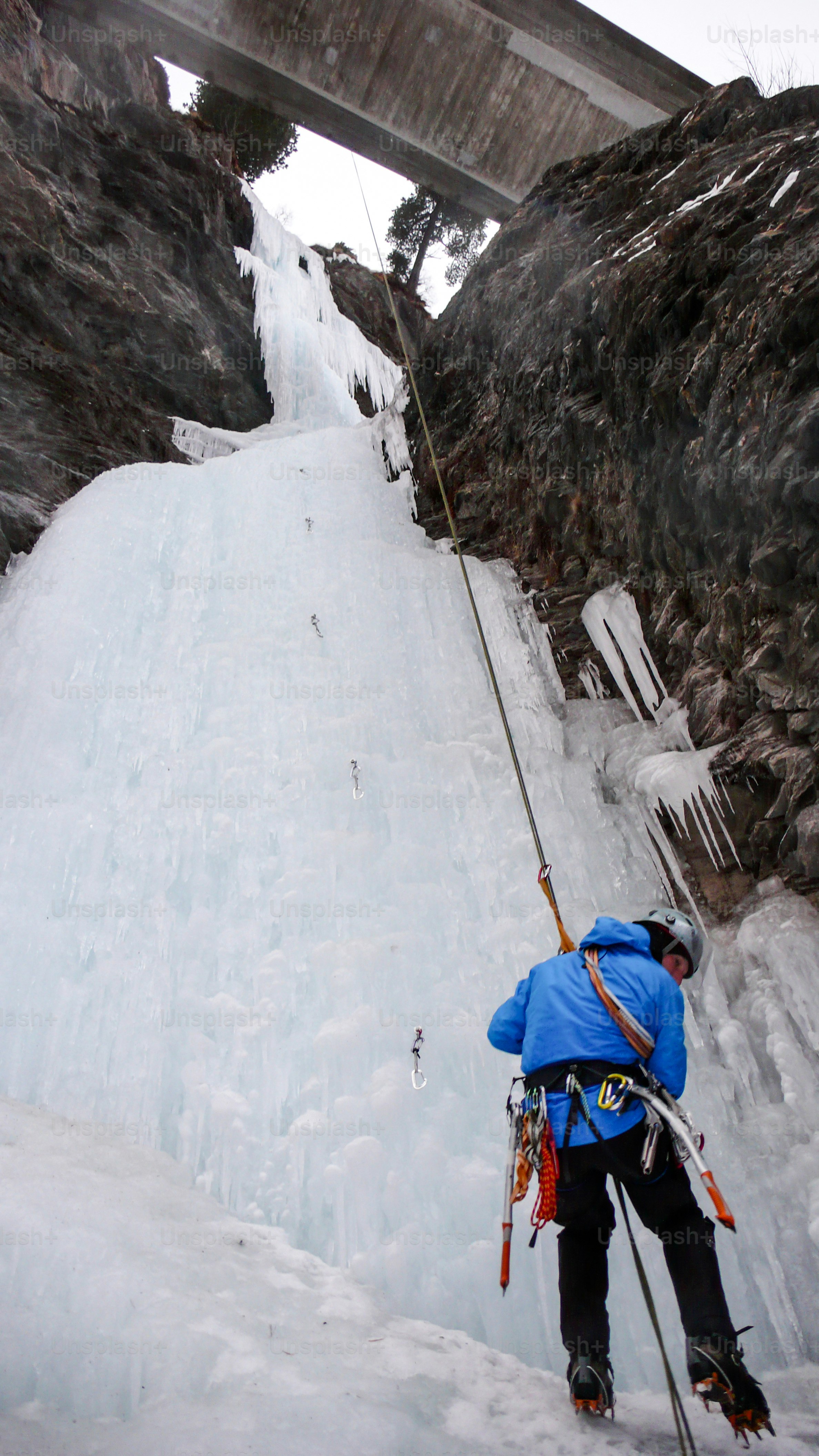 Male ice climber in a blue jacket rappelling a frozen waterfall in the ...