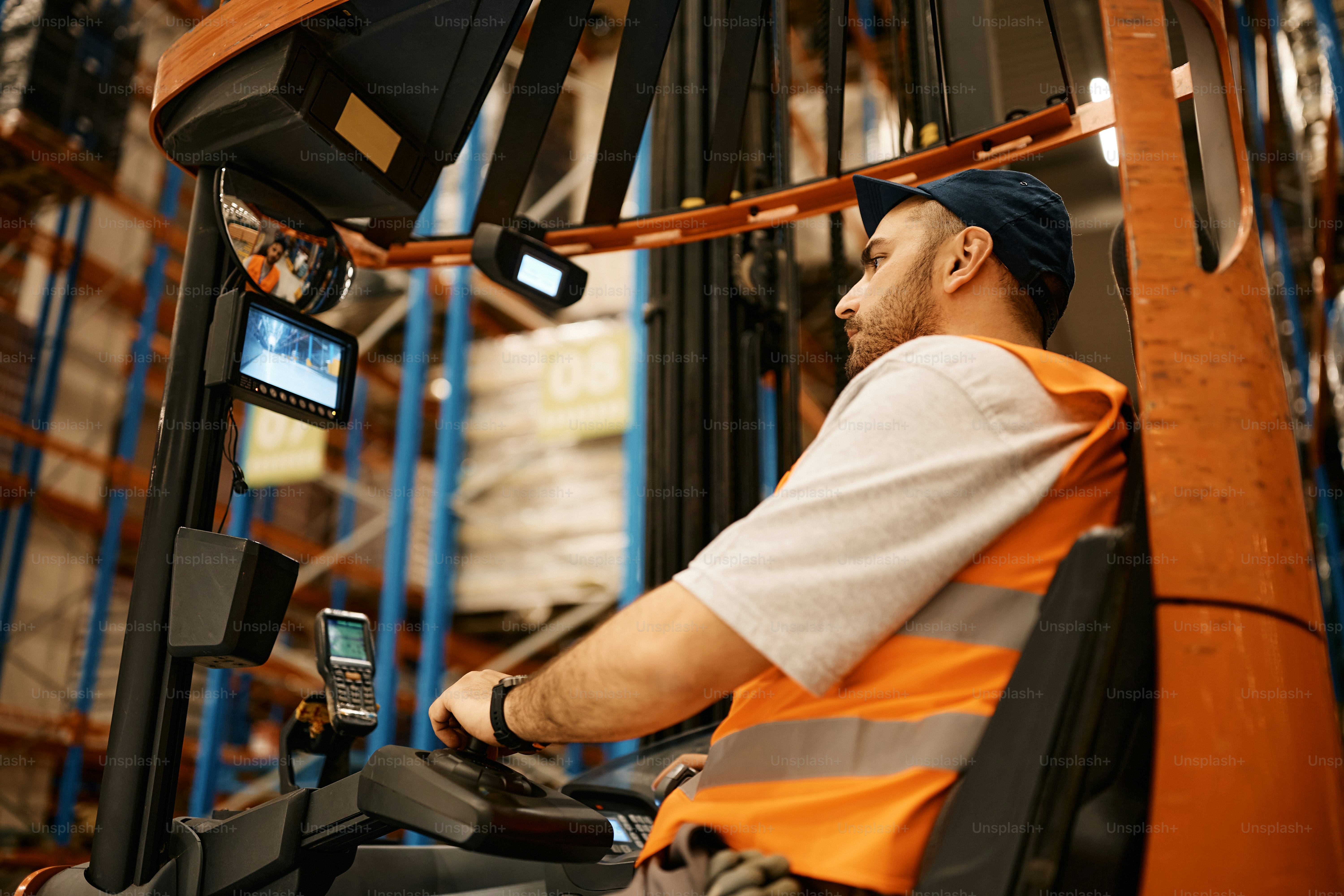 Young warehouse worker driving forklift through storage compartment ...