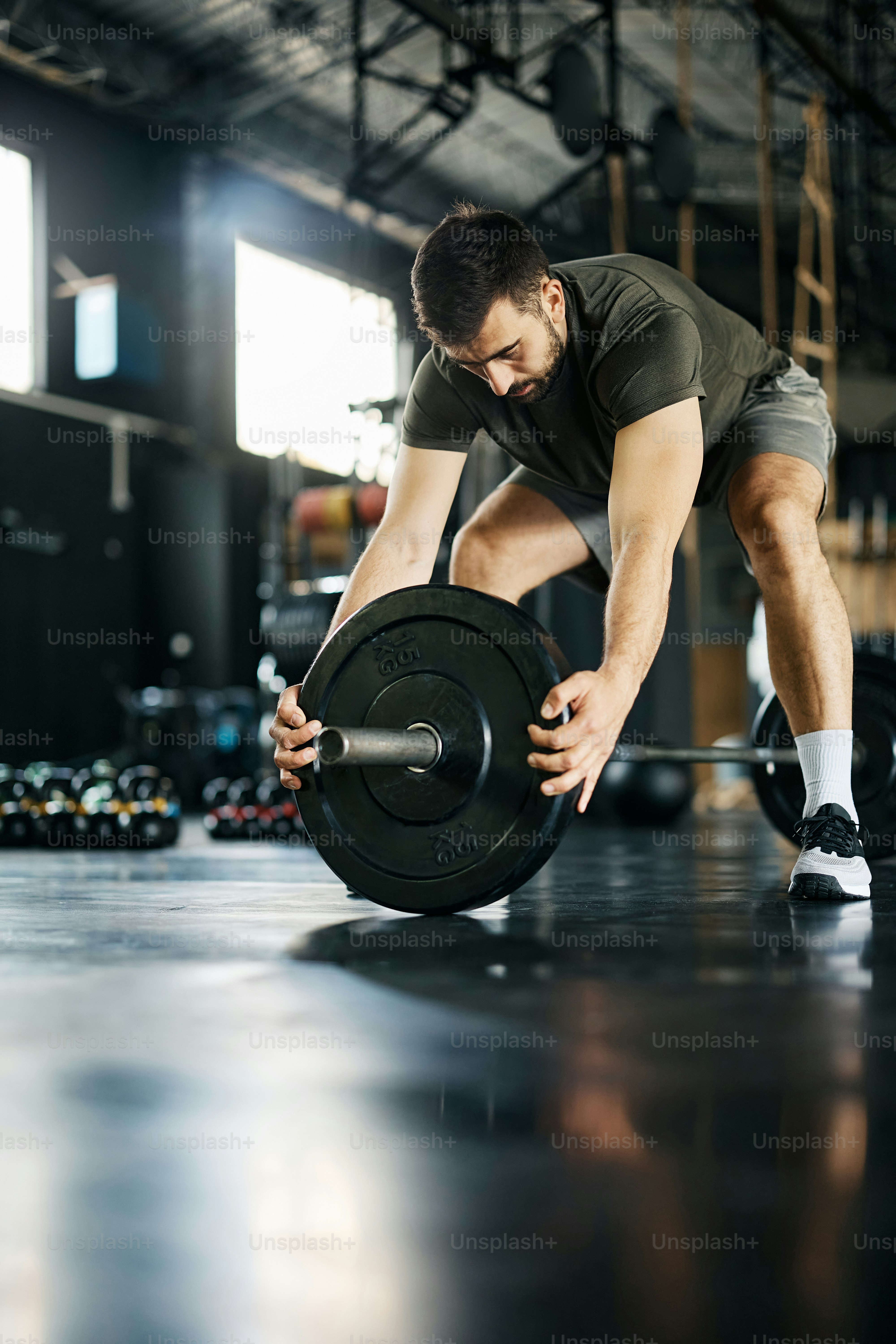 Athletic man putting weight disk on barbell before strength training in ...