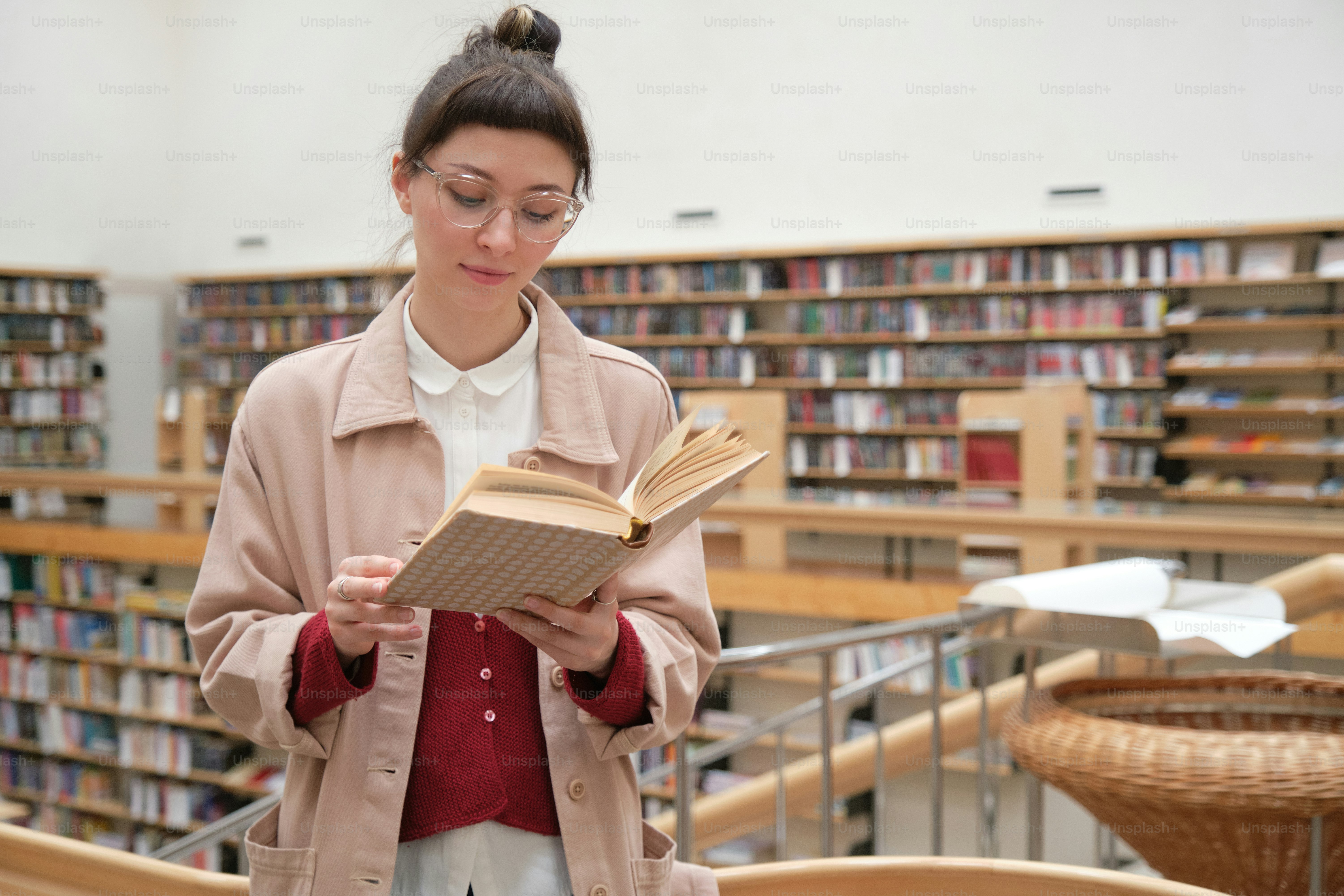 Serious young woman examining the book while standing in the big ...