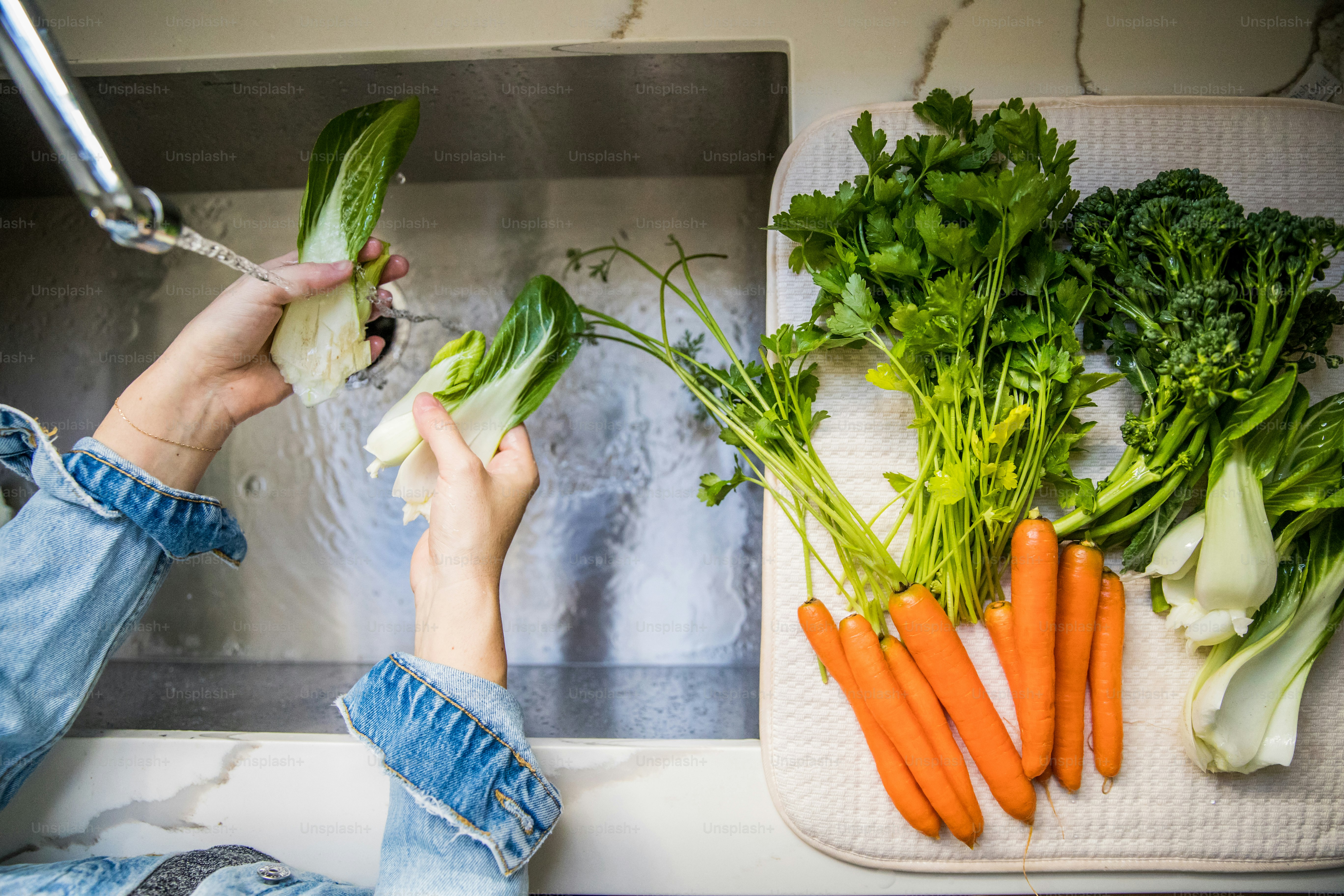 Woman washing and drying fresh vegetables from grocery delivery in sink ...