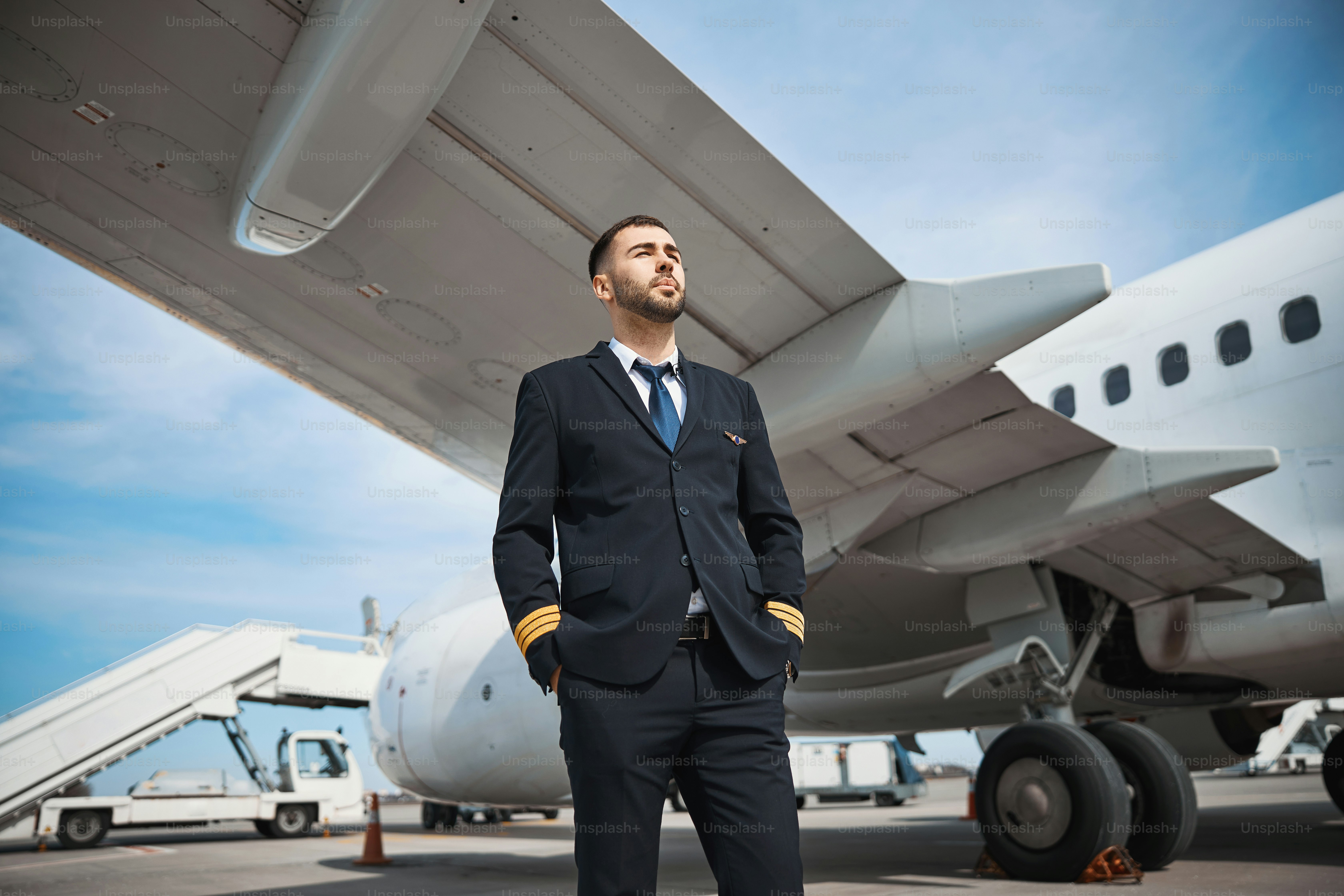 Experienced airplane captain placing hands in his pockets while ...