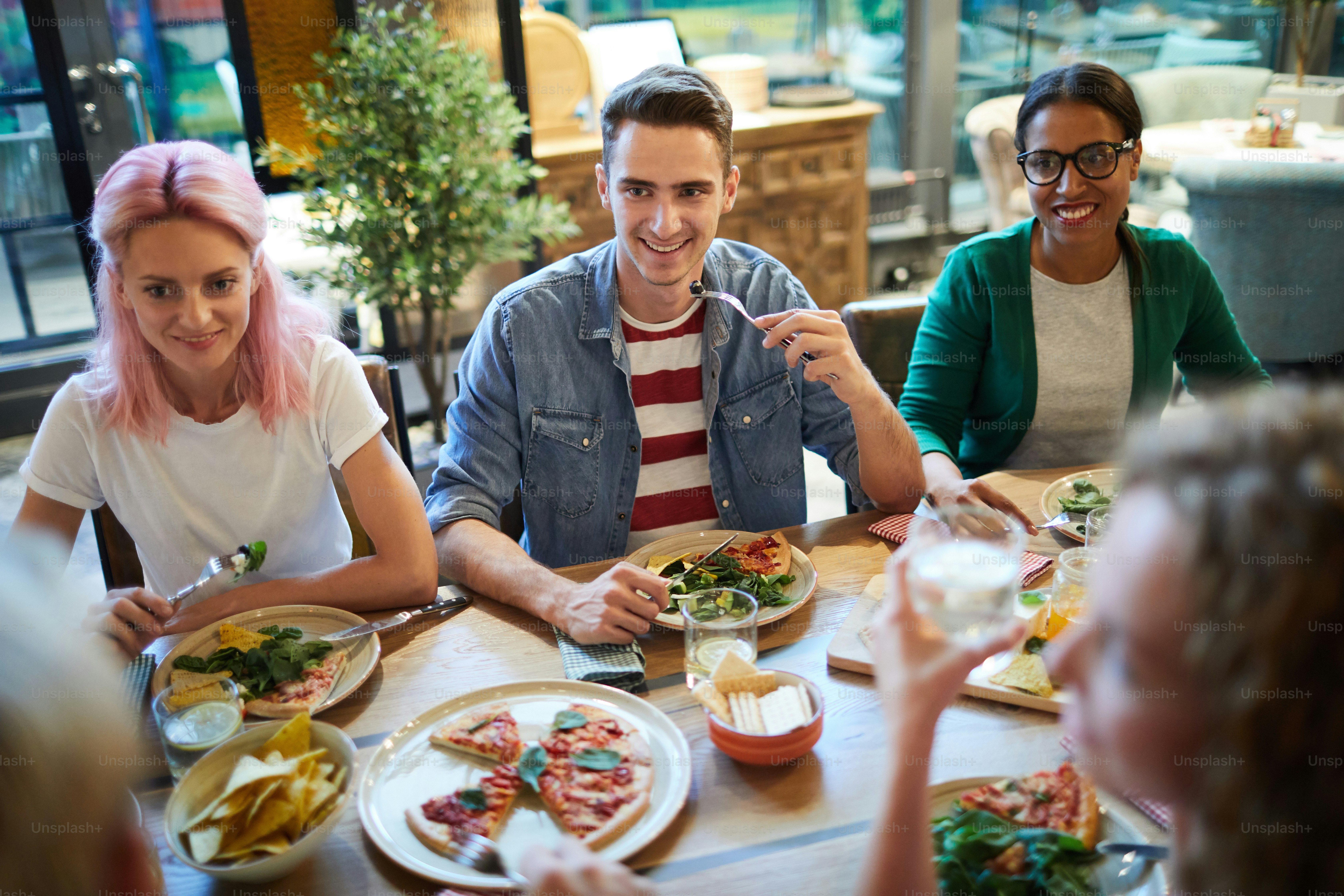 Cheerful intercultural young people gathered by cafe or restaurant for ...
