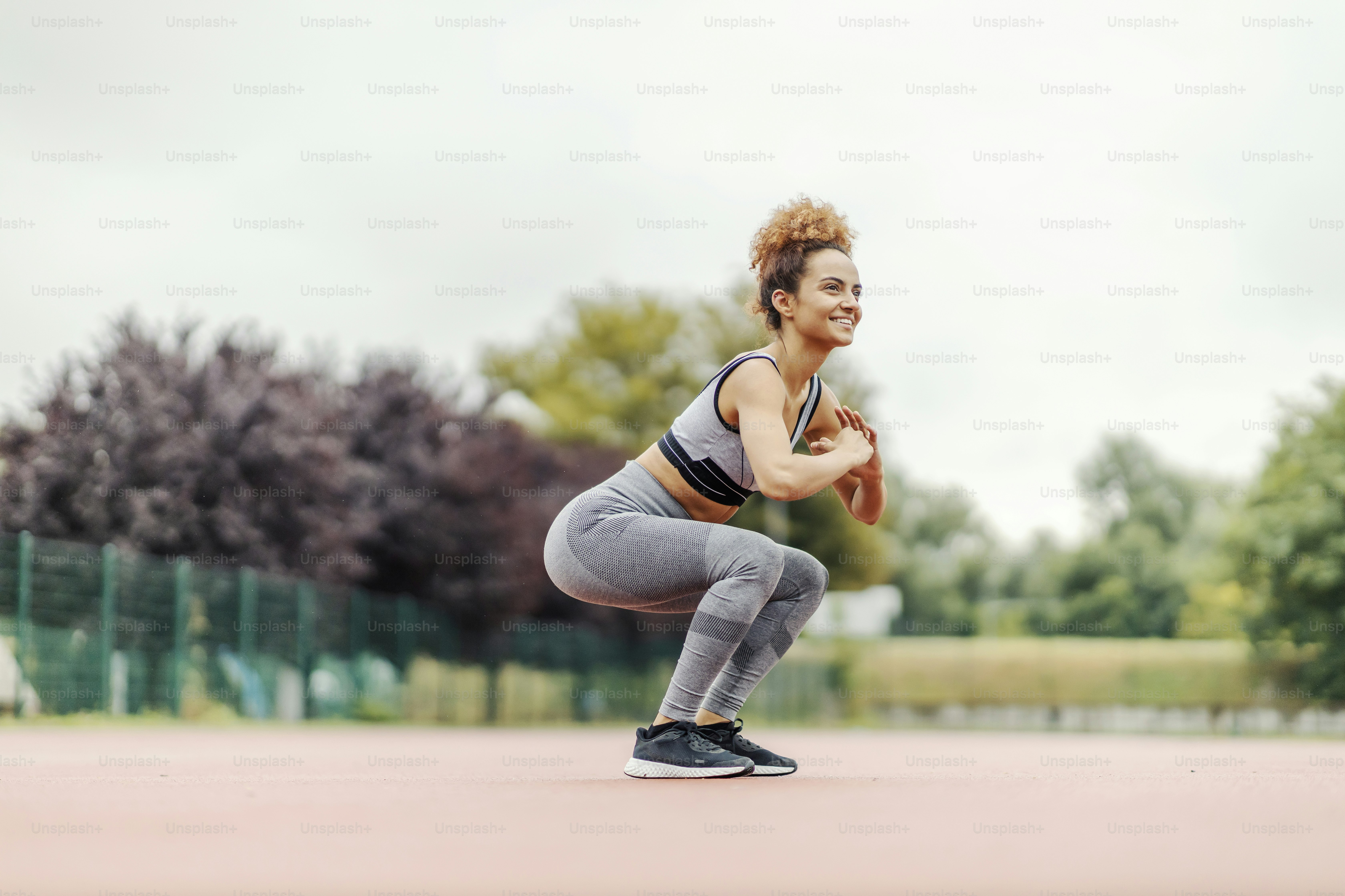 A fit, dedicated sportswoman is doing squats endurance in the stadium ...