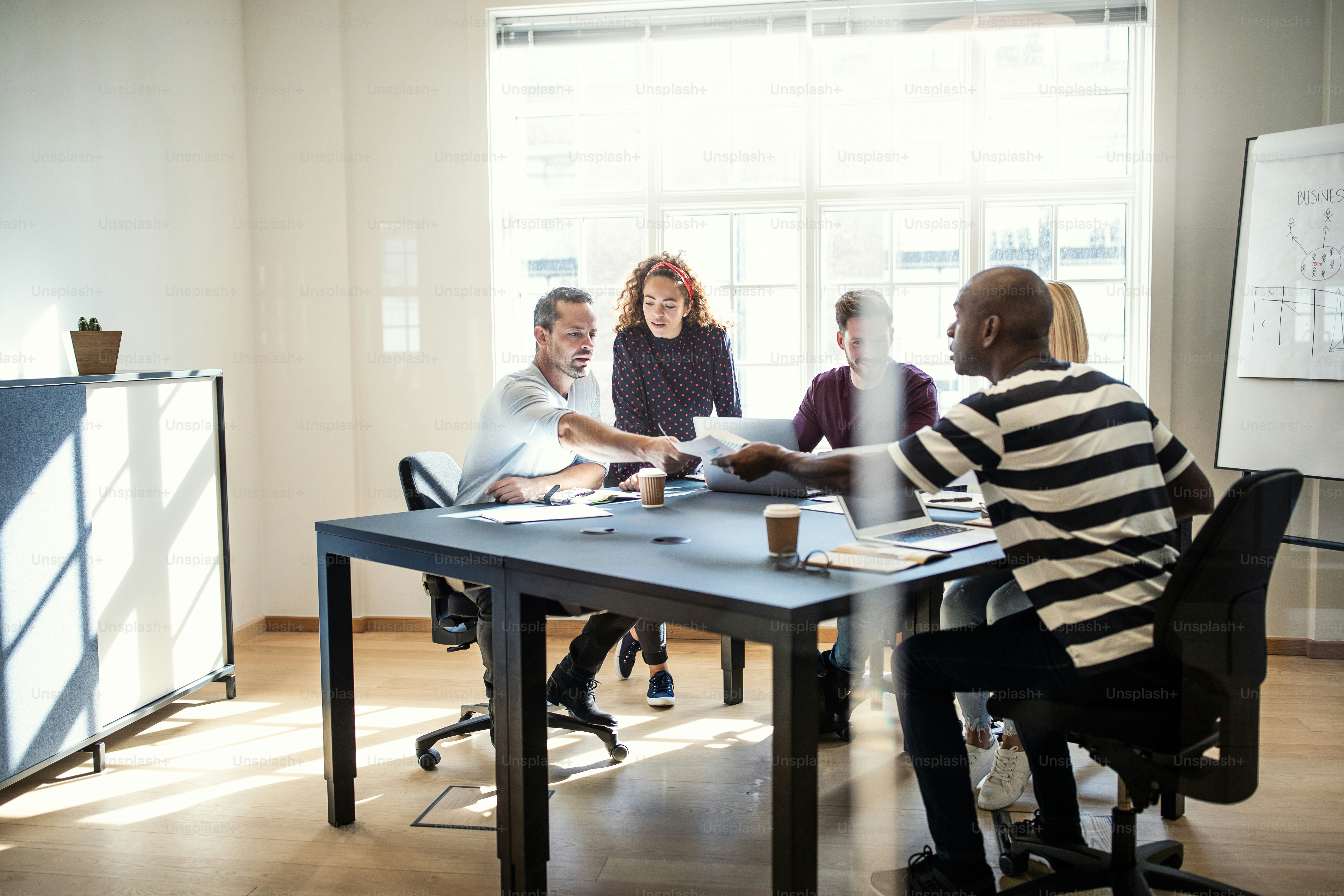 Group of diverse designers discussing paperwork together while sitting ...