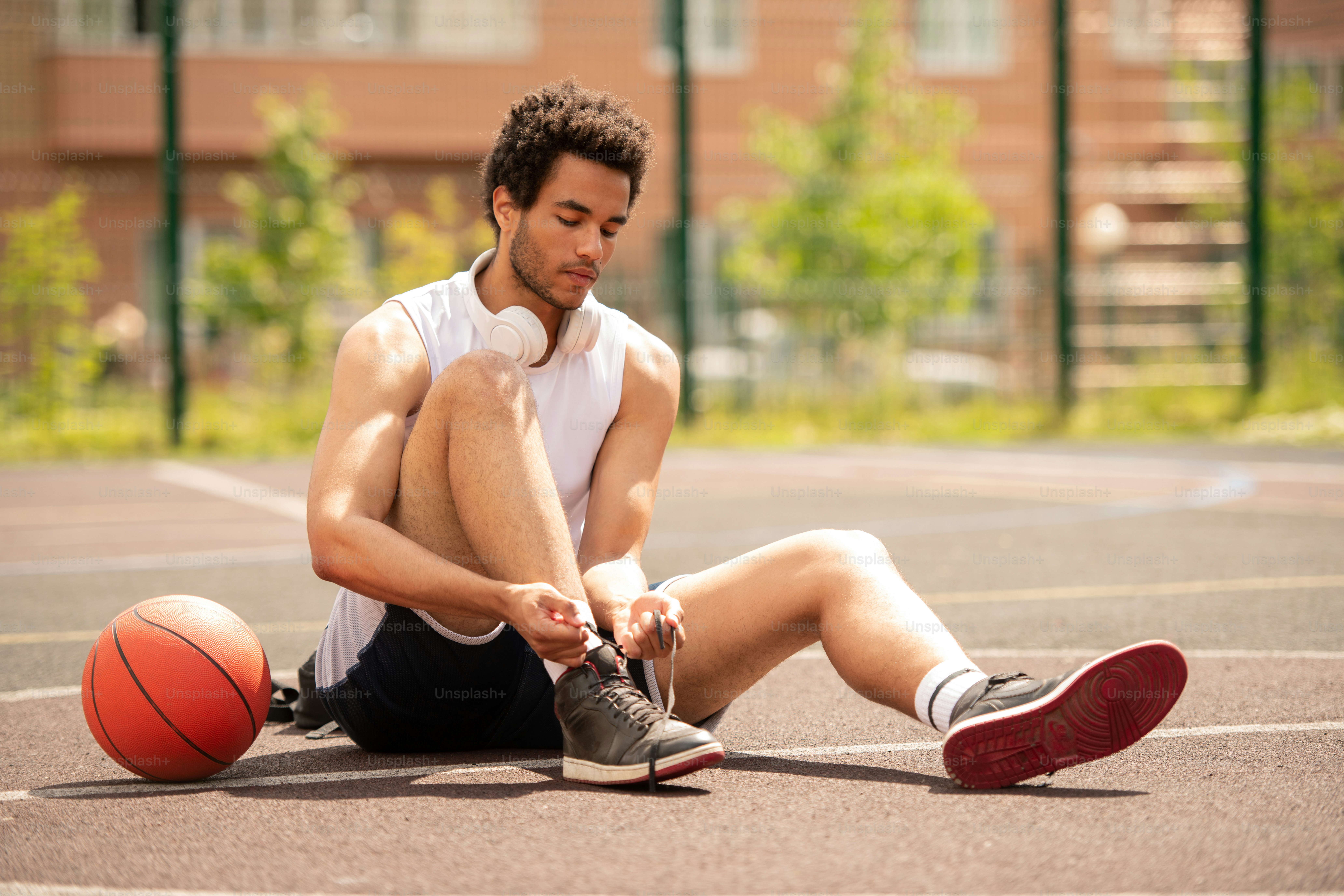 Young mixed-race athlete in sportswear sitting on basketball court and ...