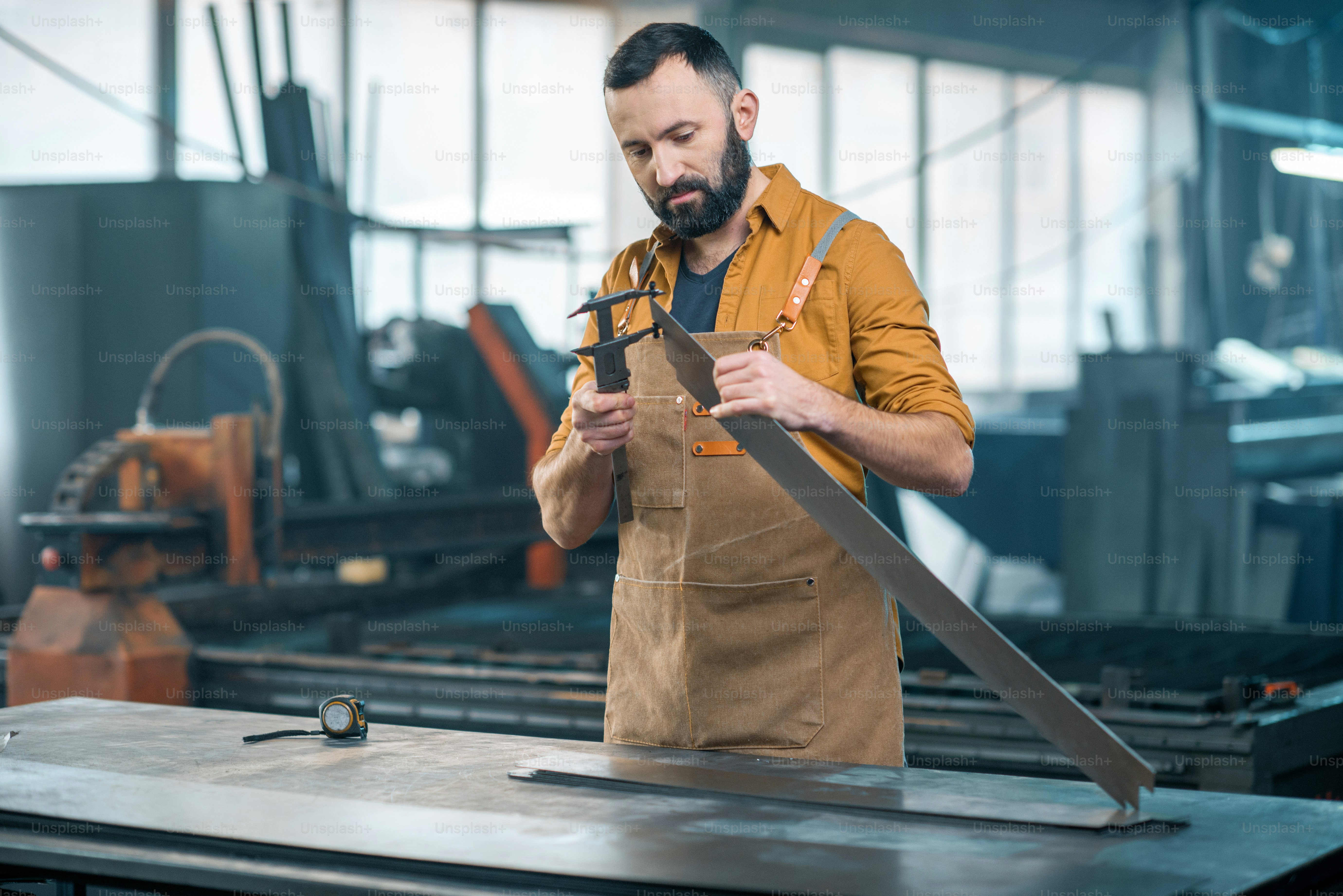Metal industry worker dressed in apron measuring some metalwork at the ...