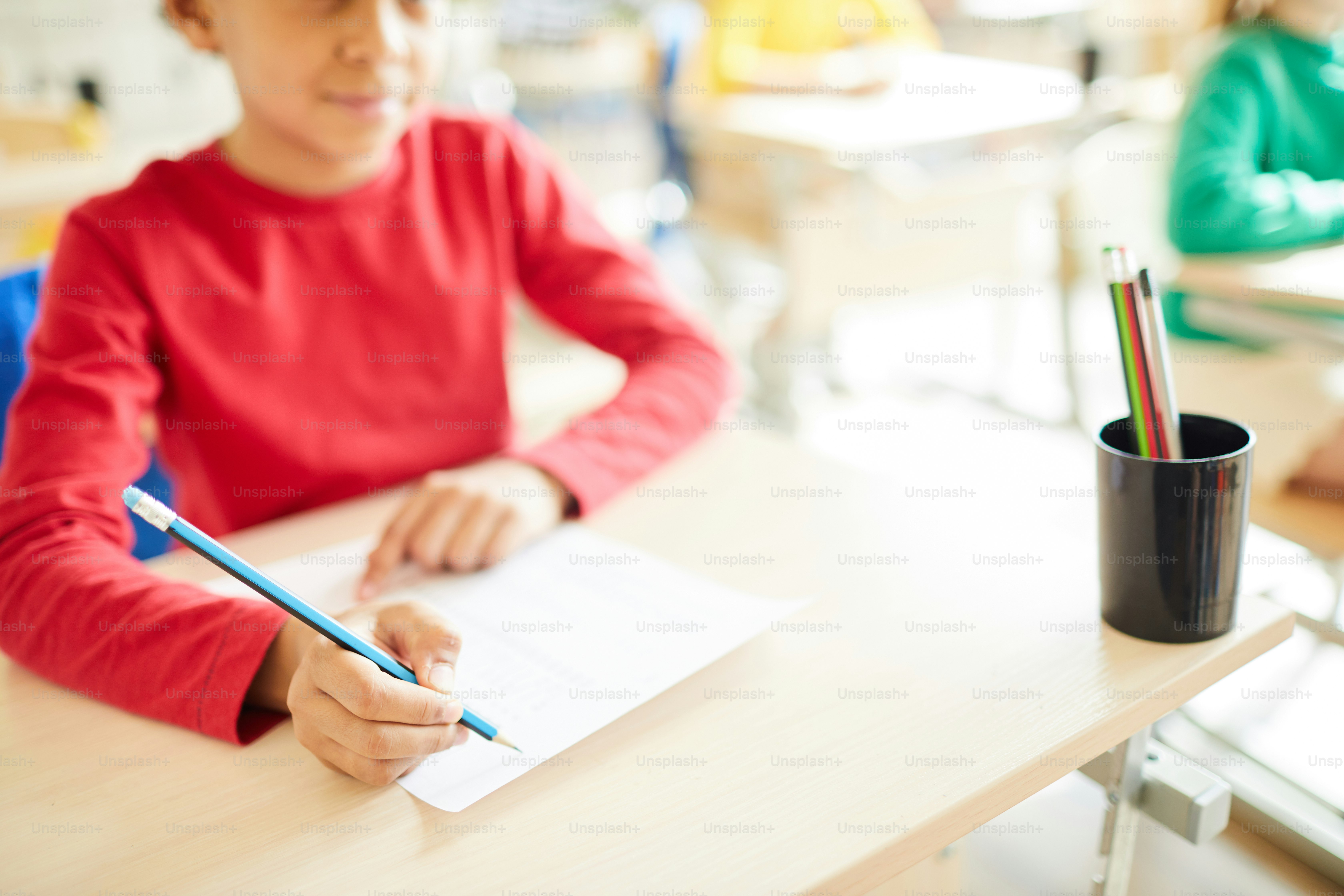 Close-up of schoolboy holding pencil and writing in paper while taking ...