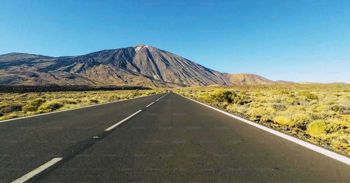 バルカンマウントと青い澄んだ空を持つ山の長い道のり 黒いアスファルトと白い線を持つ地面の視点 運転と旅行のコンセプトの写真