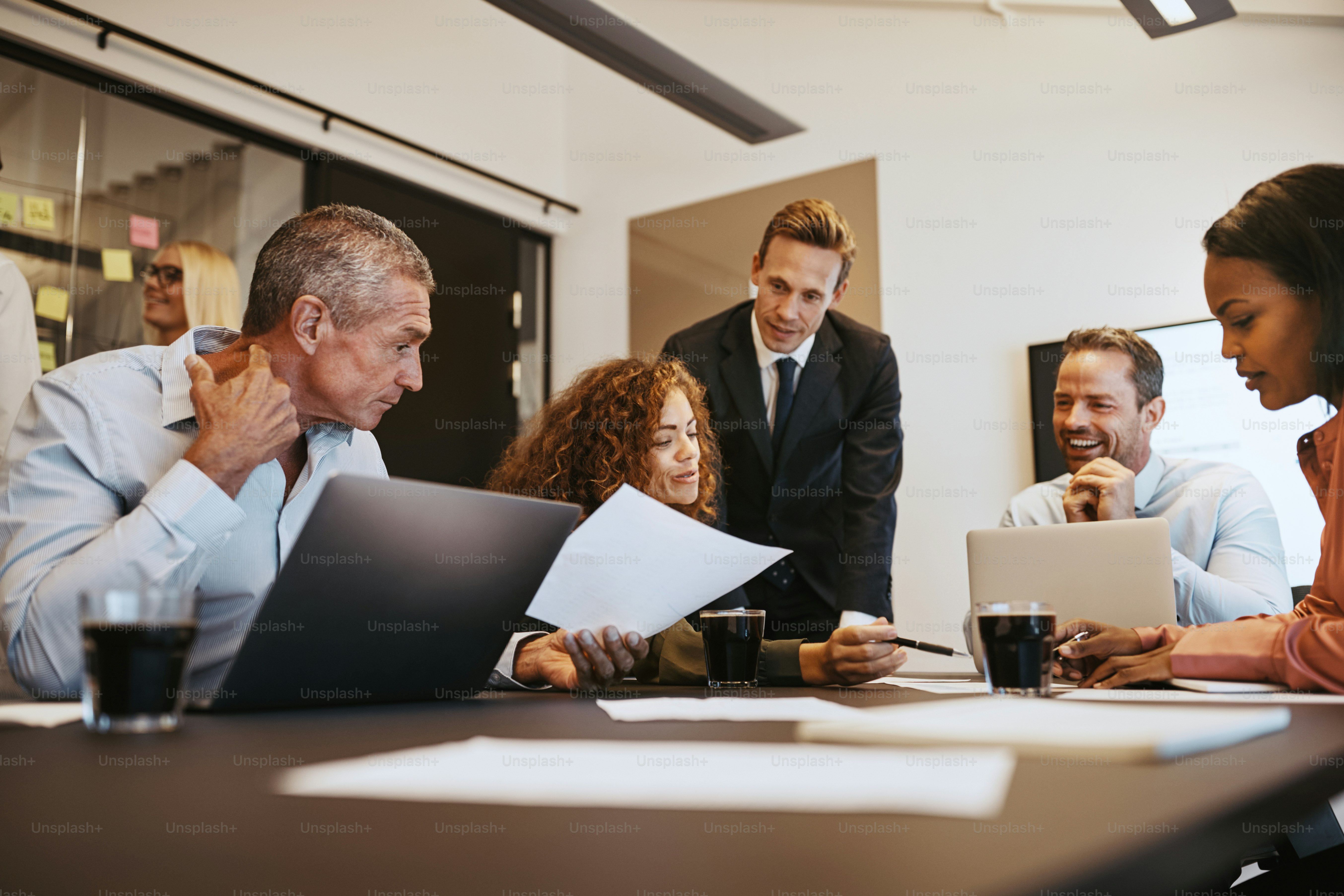 Group of diverse designers discussing paperwork together while sitting ...