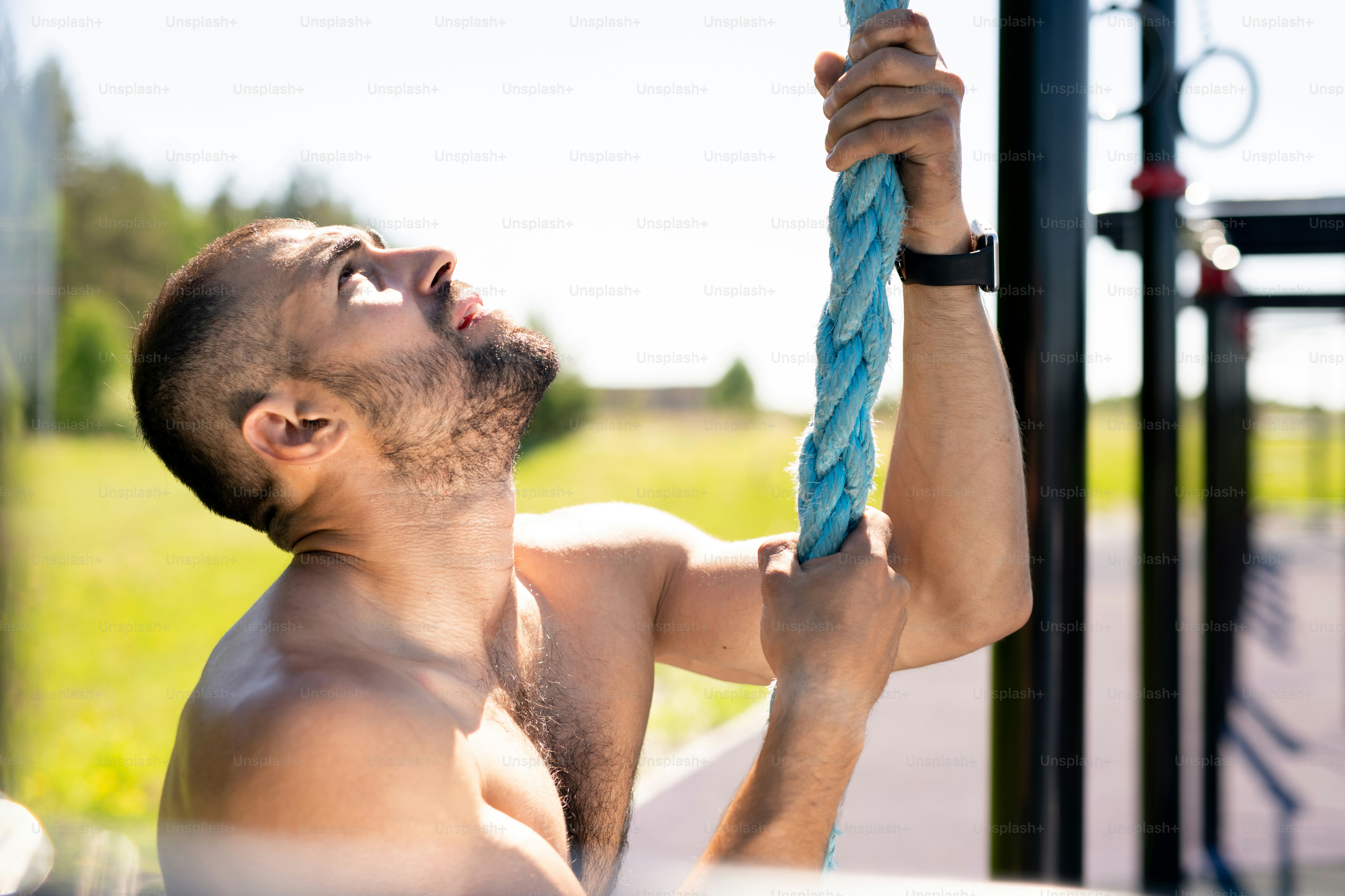 Young muscular sportsman looking upwards while holding end of thick ...