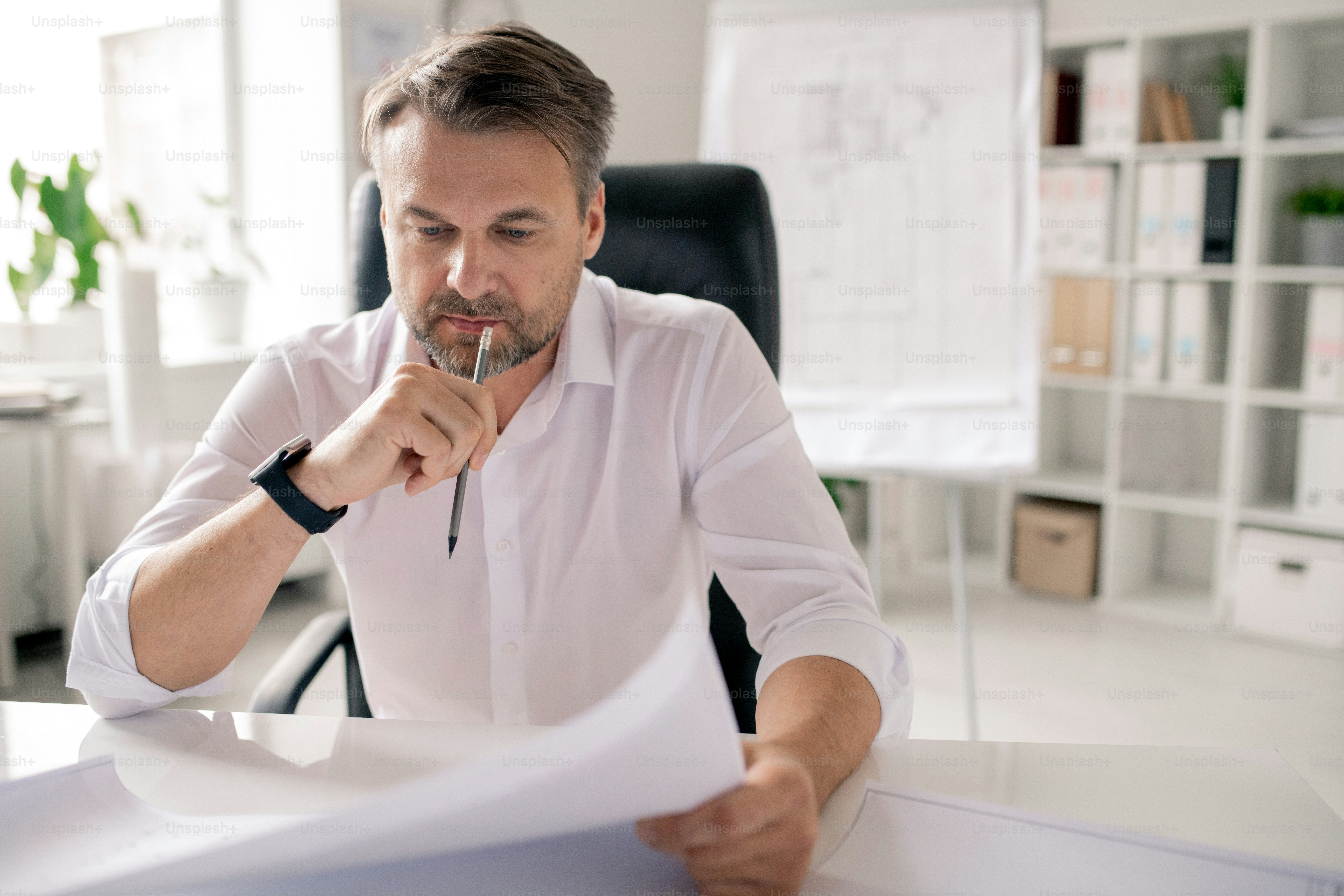 Mature pensive engineer with pencil and paper looking at sketch while ...