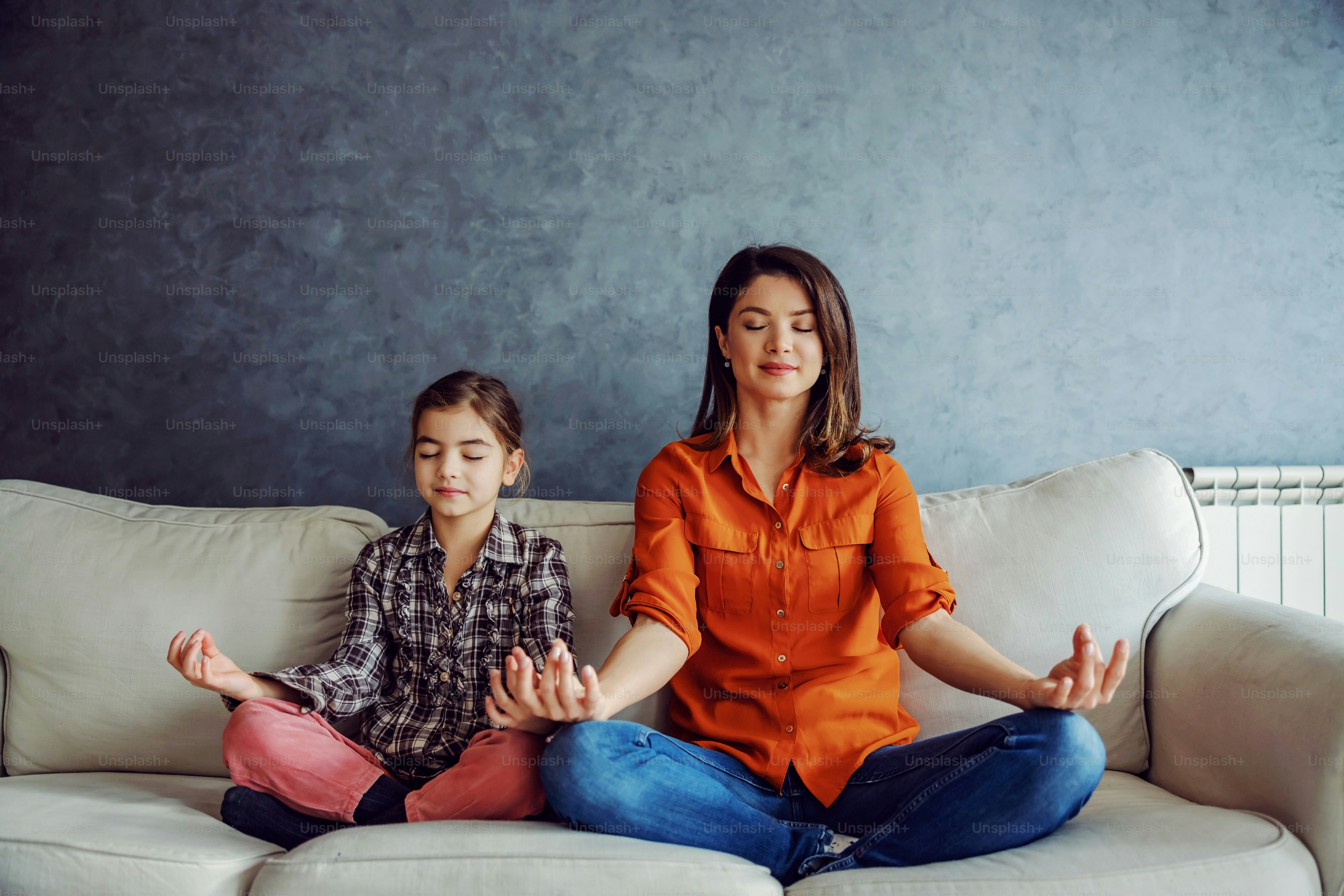 Calm mother and daughter sitting on the sofa in lotus position and ...