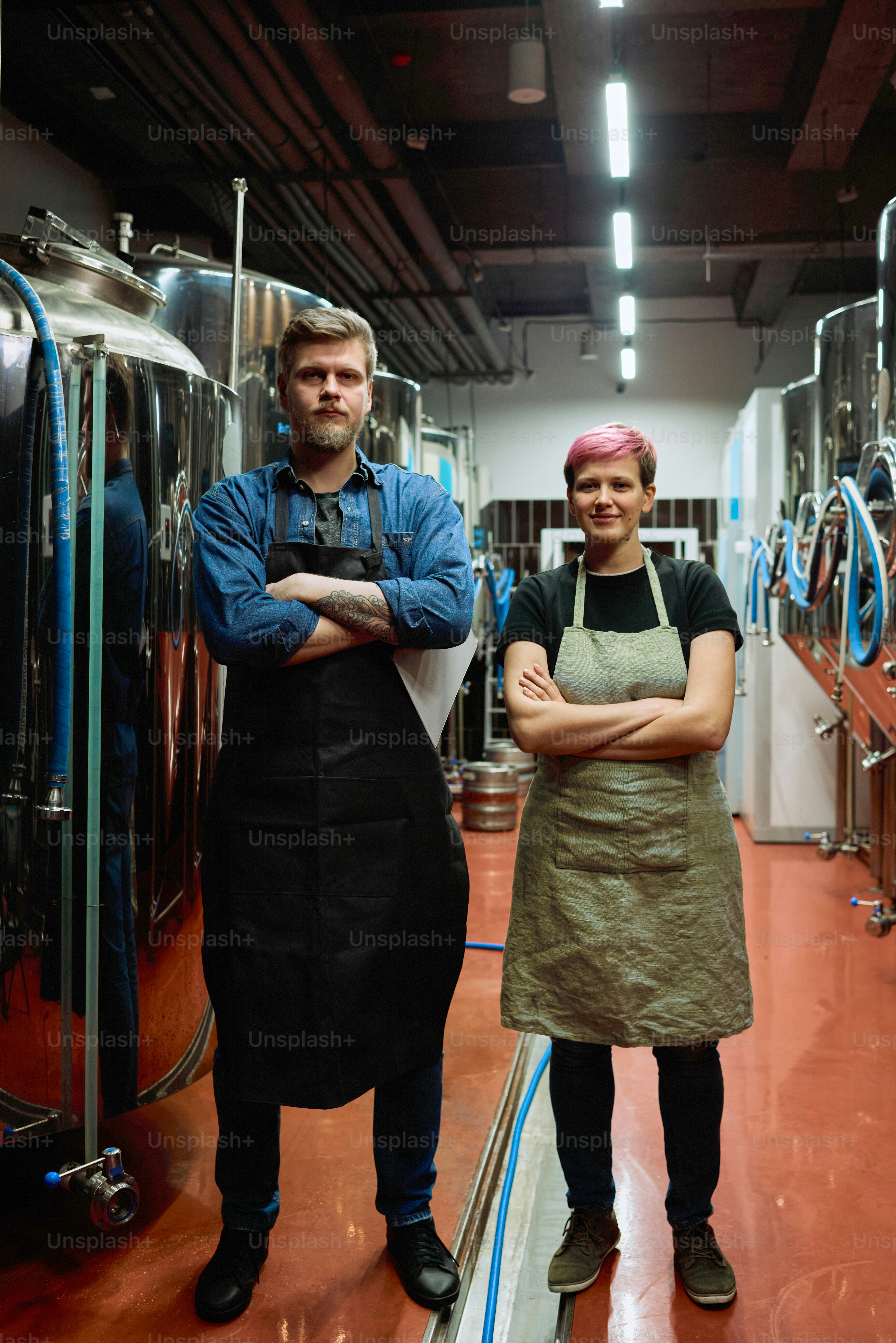 Young male and female workers of beer production factory in aprons ...