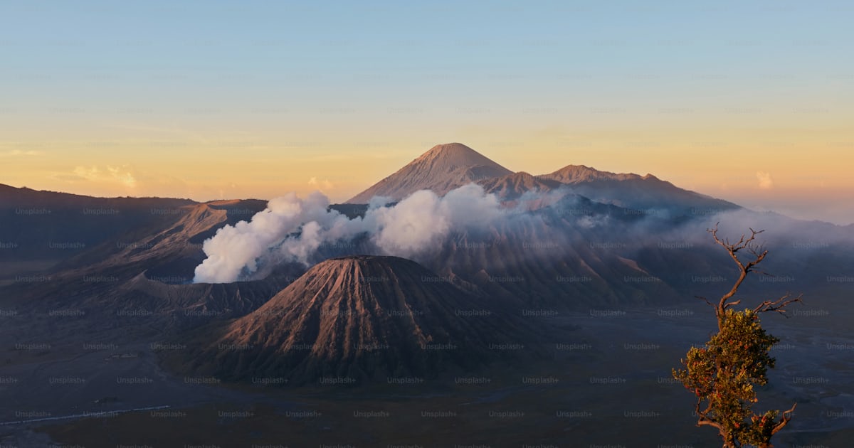 クレーターの深さを持つ煙の雲の中の活火山。インドネシアの東ジャワにあるグヌンブロモ火山の後ろの日の出。の写真 自然 Unsplashの写真