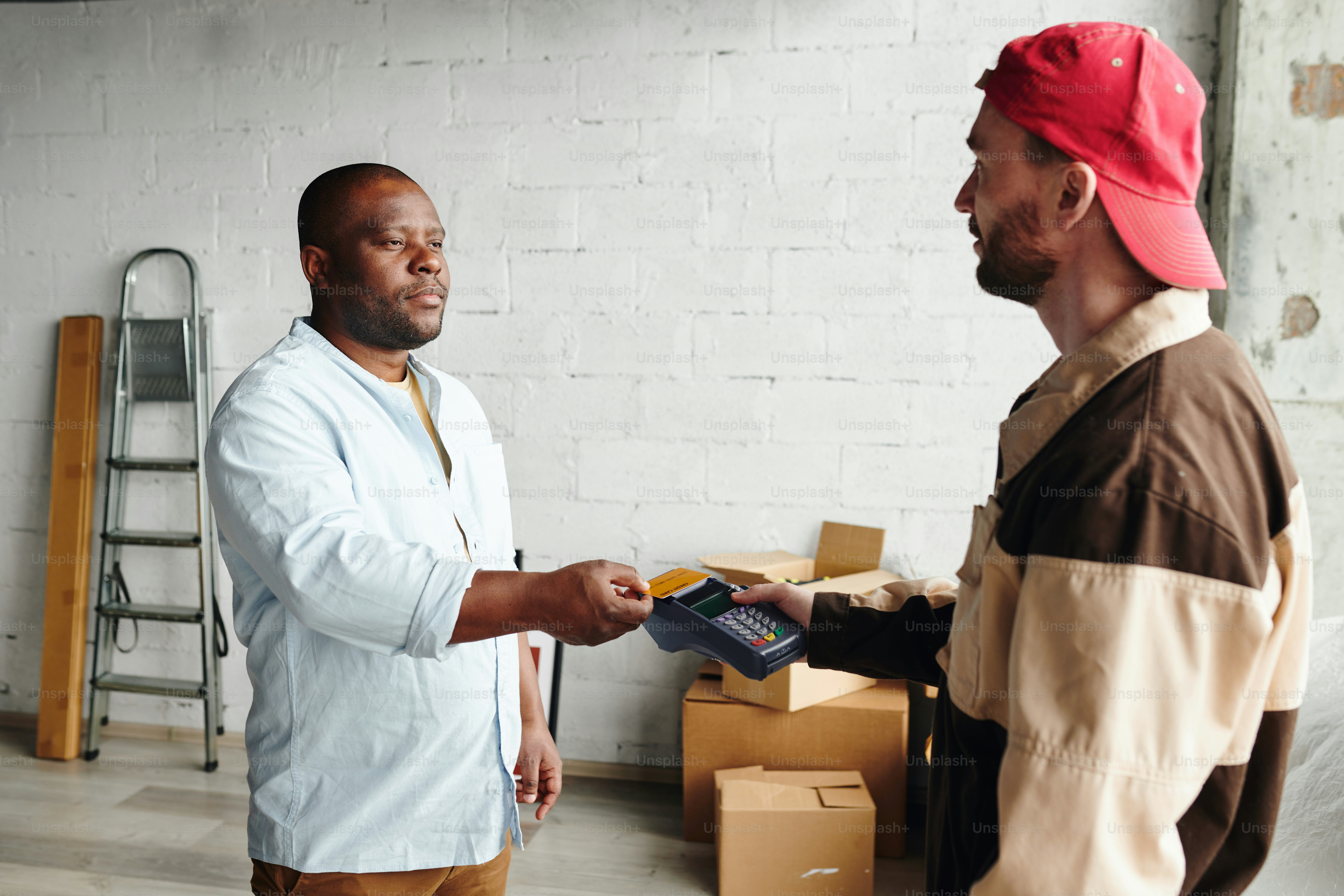 Young loader in workwear holding terminal while African male client ...