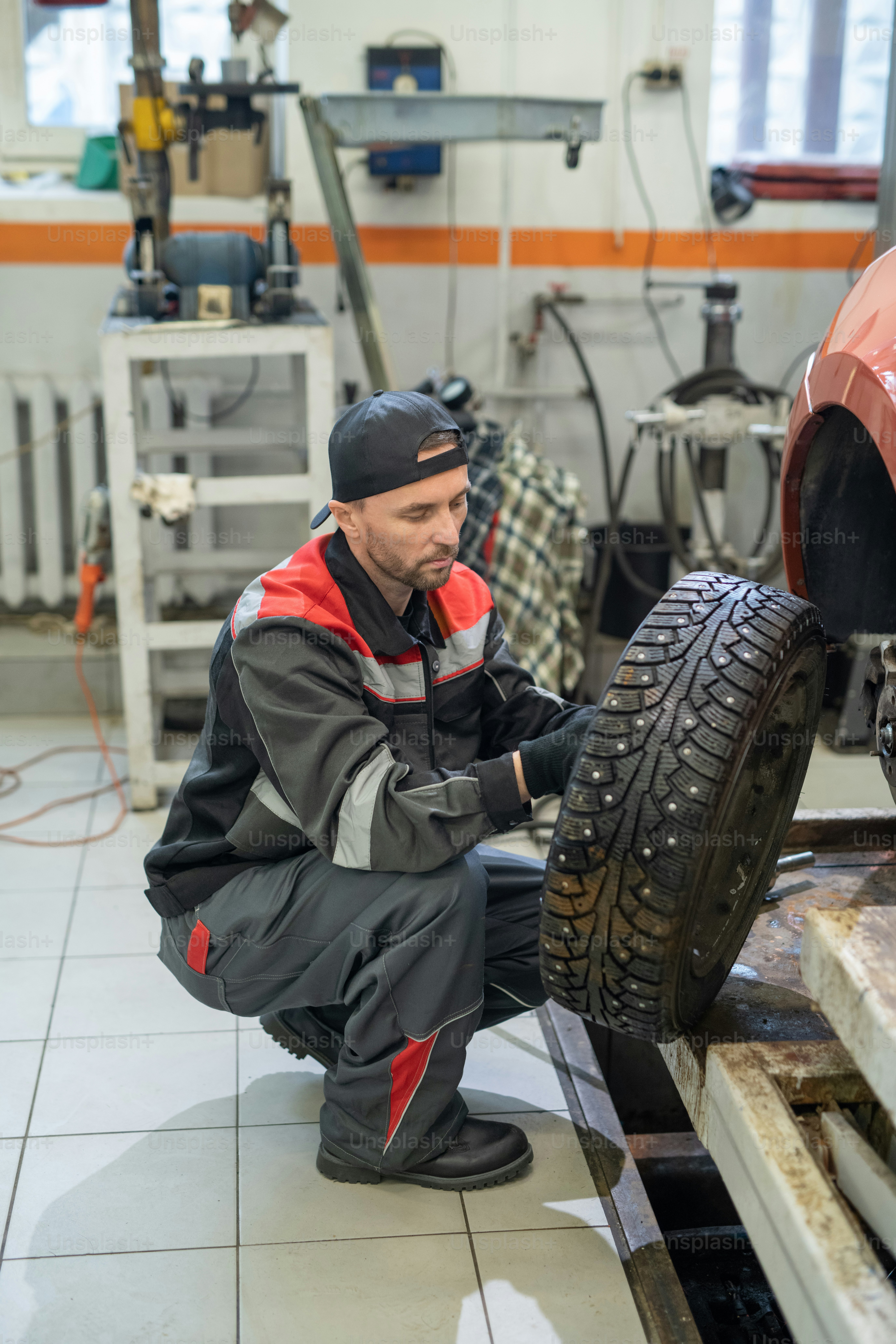 Vertical full length portrait of male mechanic changing tires on car ...
