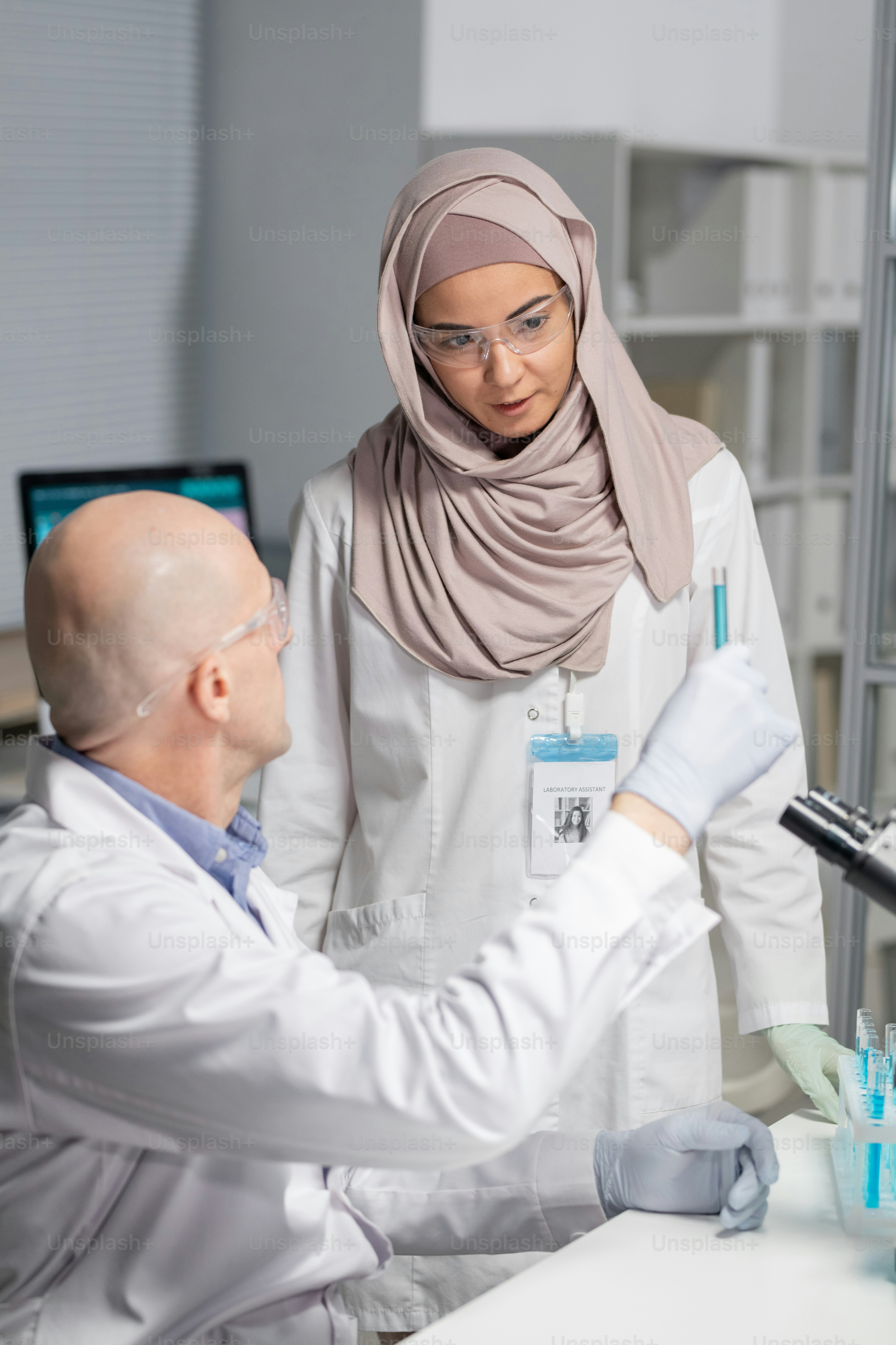 Young Muslim female virologist in hijab and whitecoat looking at blue ...