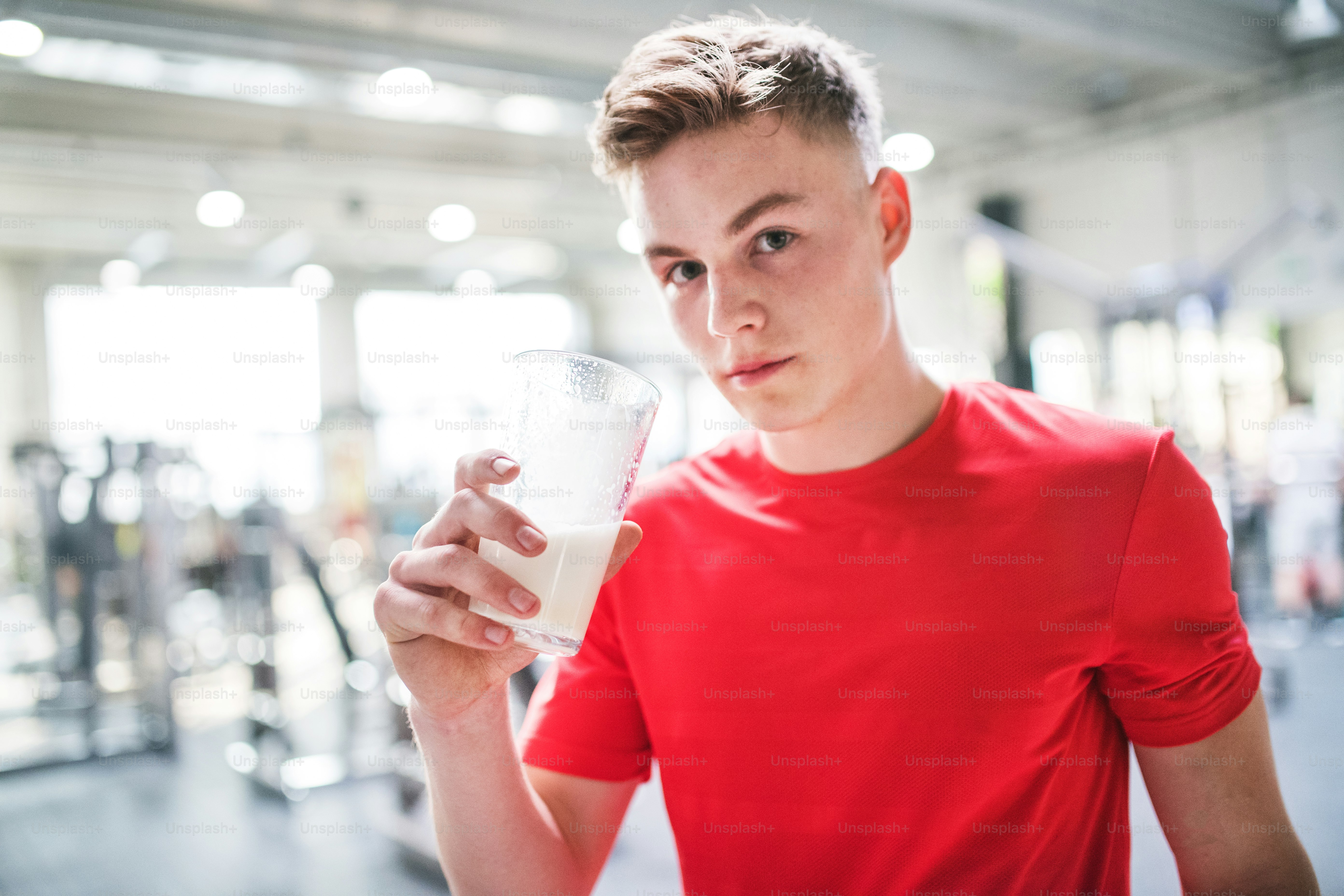 A young fit men in gym holding a glass with protein drink. Copy space ...