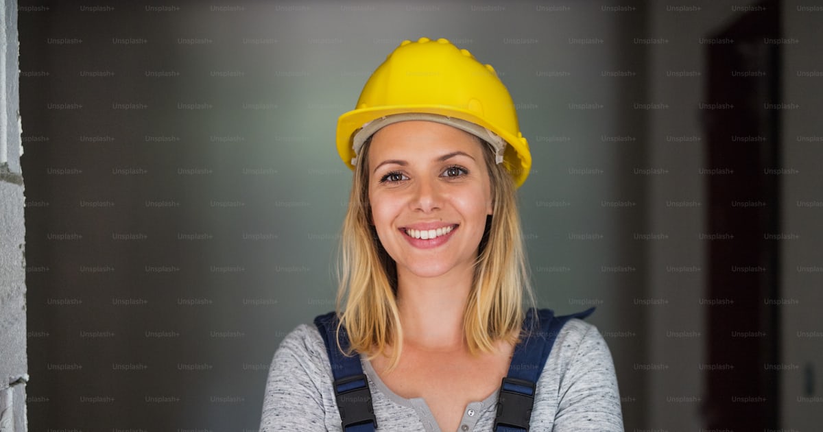 建設現場の女性作業員。黄色いヘルメットをかぶり、腕を組んだ美しい若い女性の腰を上げた肖像画。の写真 スロバキア Unsplashの写真
