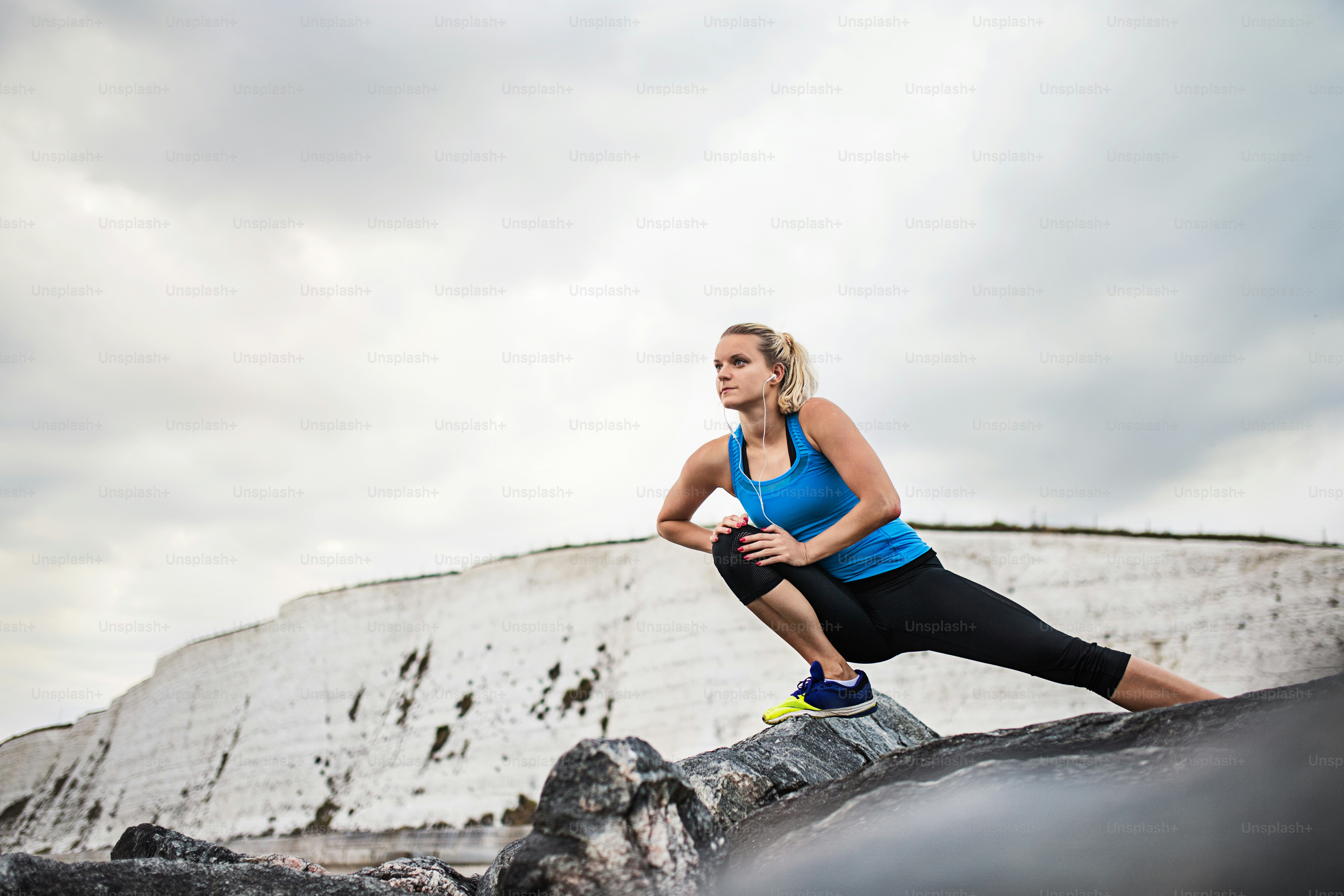 Young sporty woman runner with earphones standing outside on the rocks ...